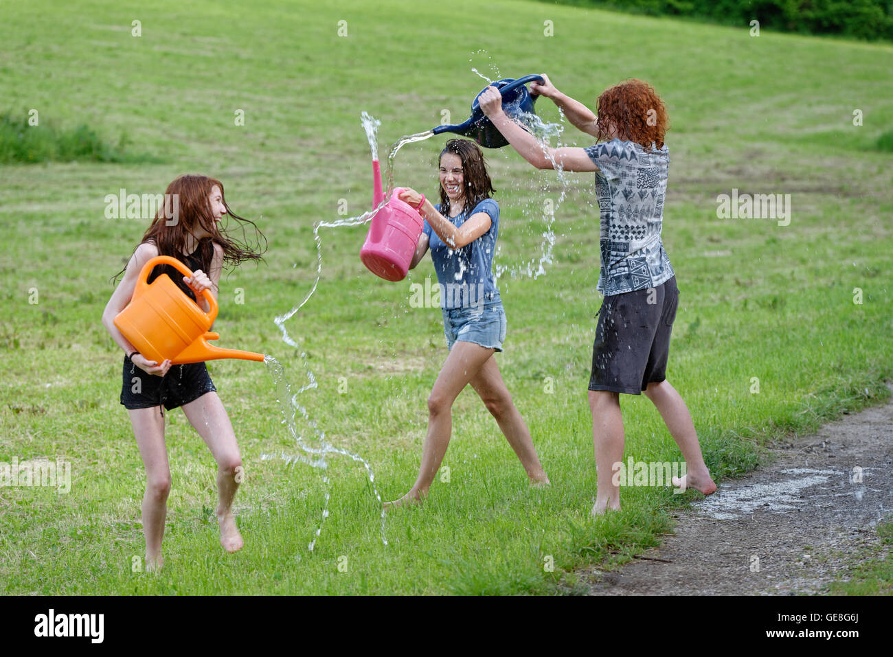 Three teenagers with watering cans splashing with water Stock Photo - Alamy