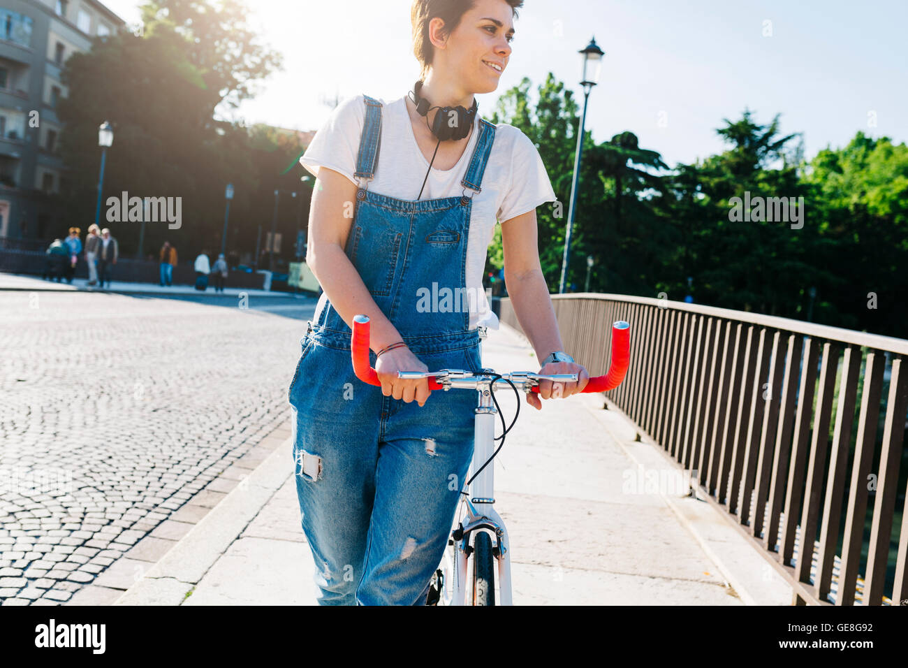 Smiling young woman pushing bicycle on bridge Stock Photo - Alamy