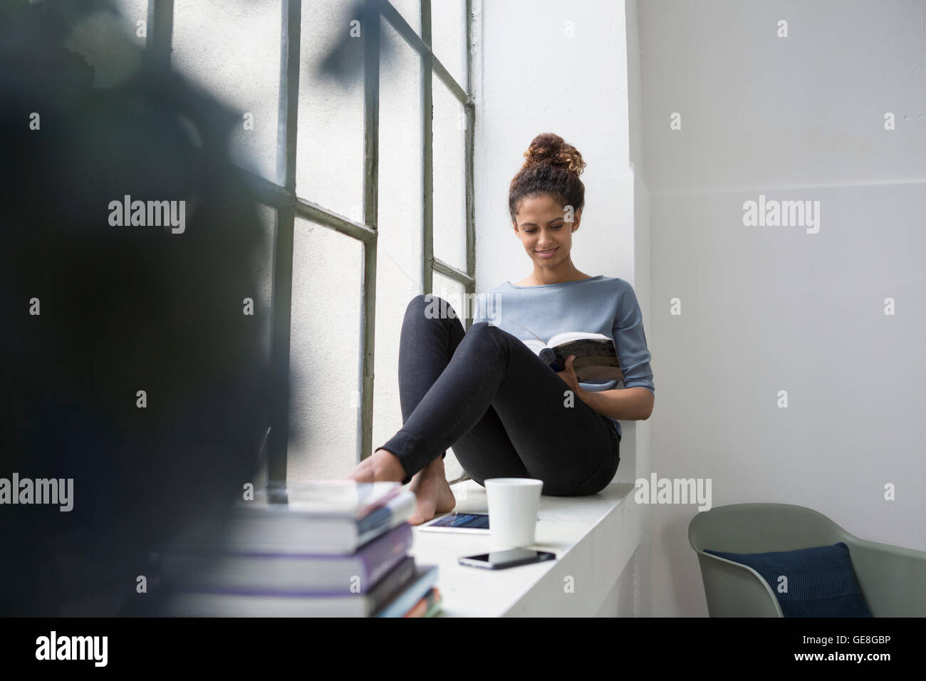 Woman sitting on window sill reading book Stock Photo - Alamy