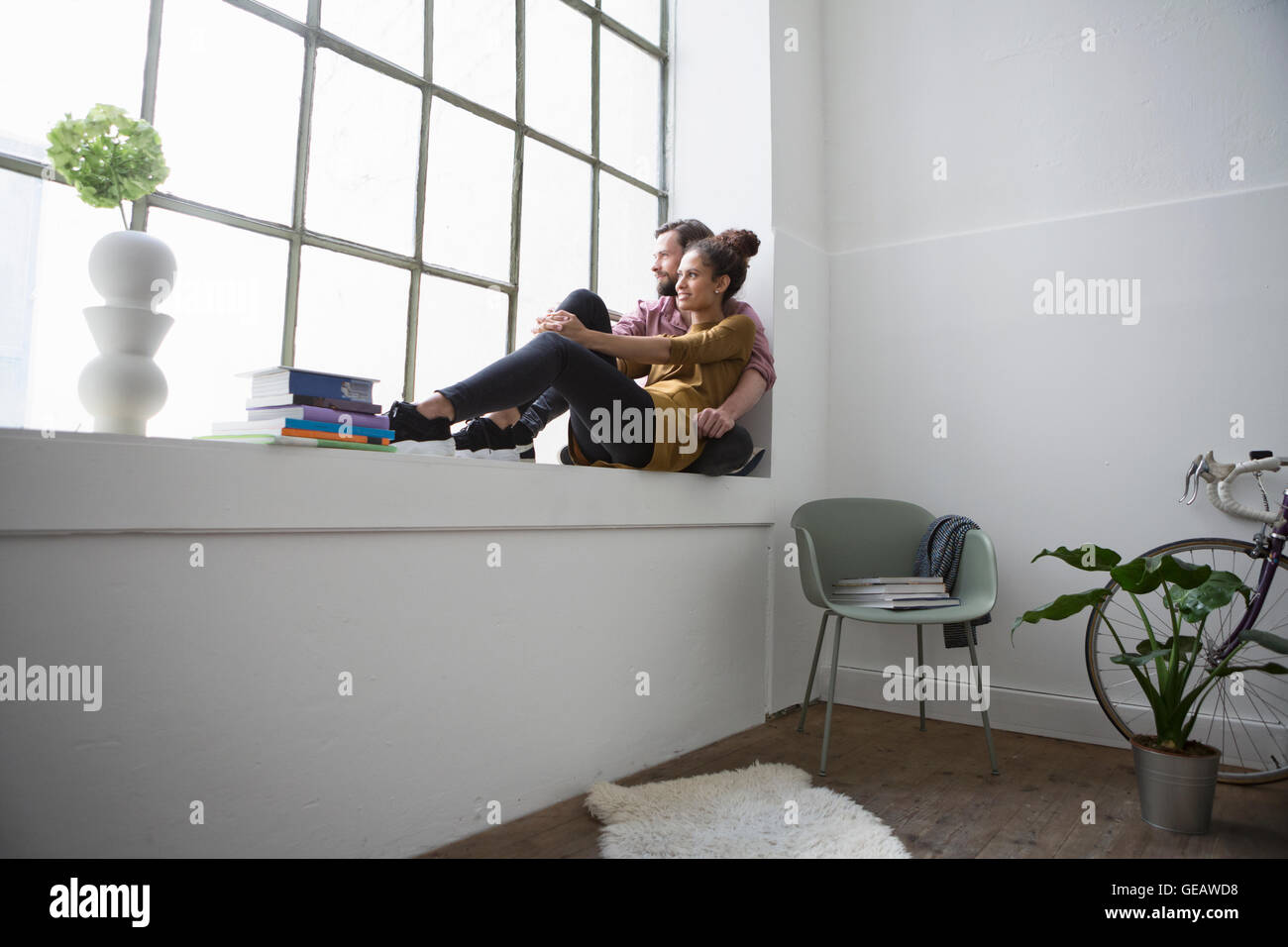 Young couple sitting on window sill with arms around Stock Photo - Alamy