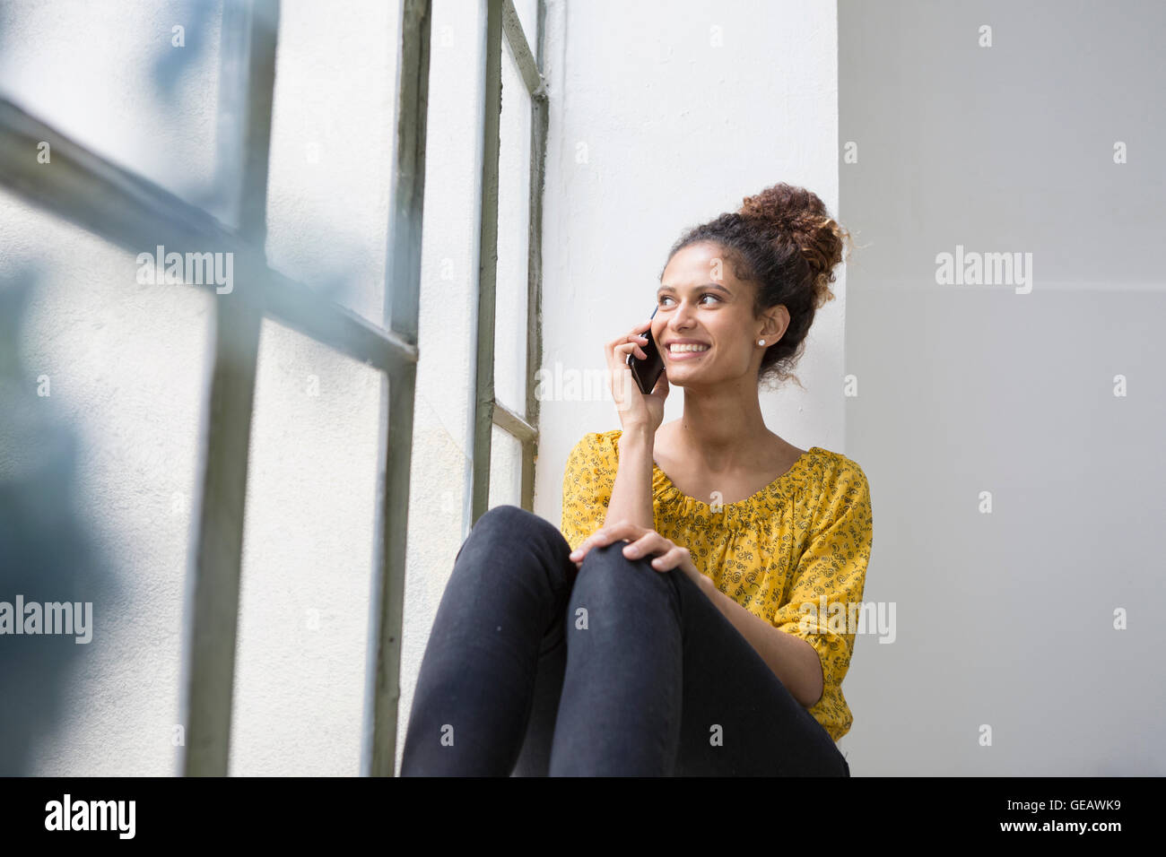 Woman sitting on window sill talking on the phone Stock Photo - Alamy