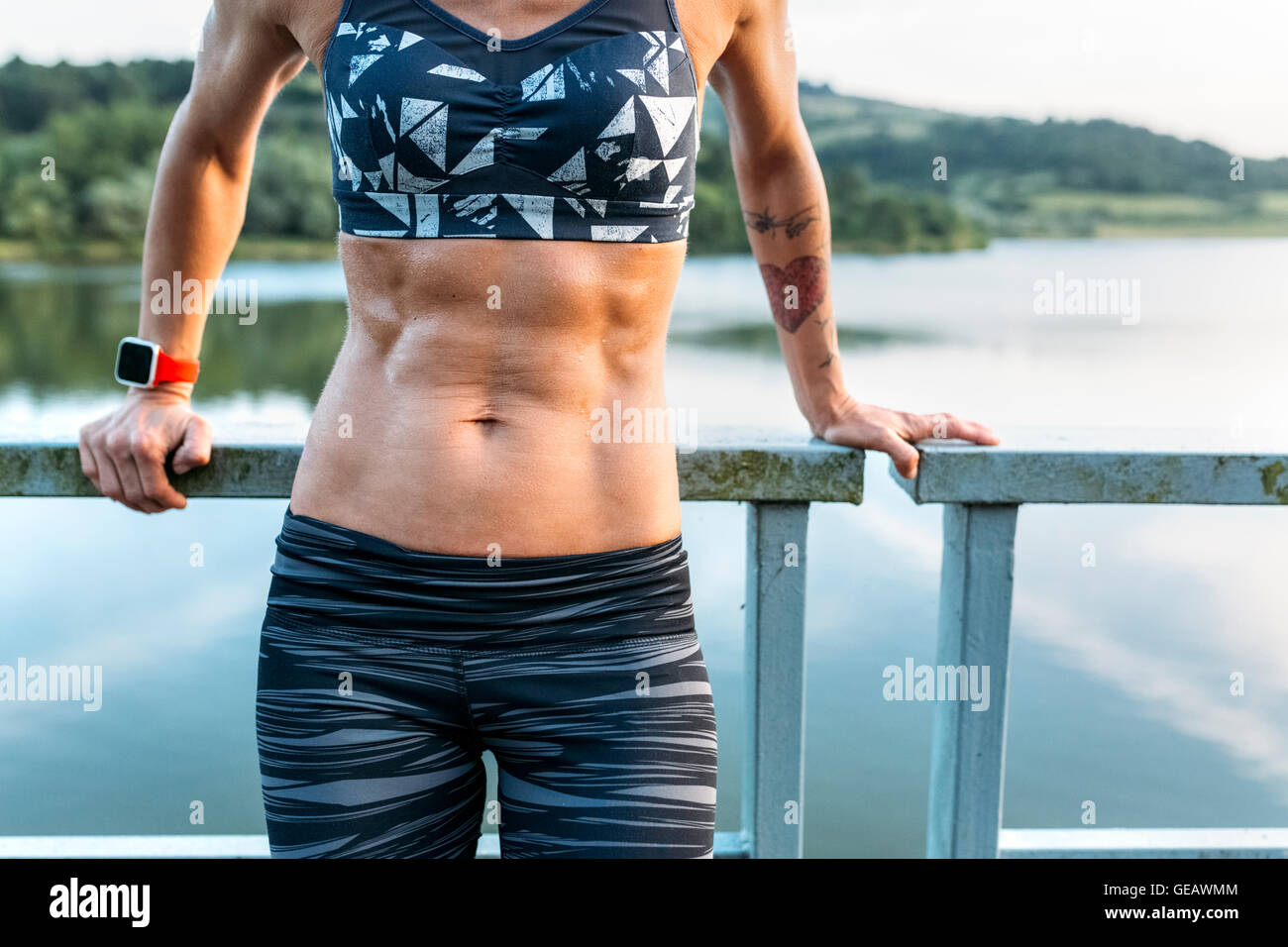 Woman leaning on railing showing abdominal muscles Stock Photo - Alamy