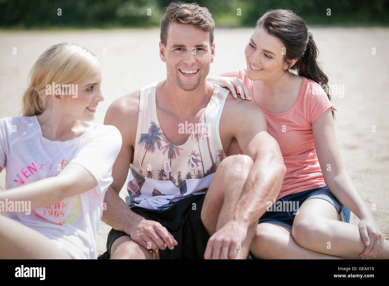 Three friends sitting on the beach having fun Stock Photo - Alamy