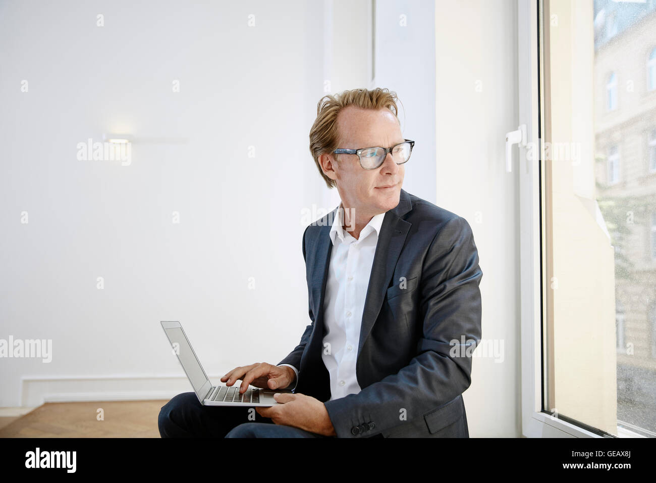 Businessman with laptop looking through window Stock Photo - Alamy