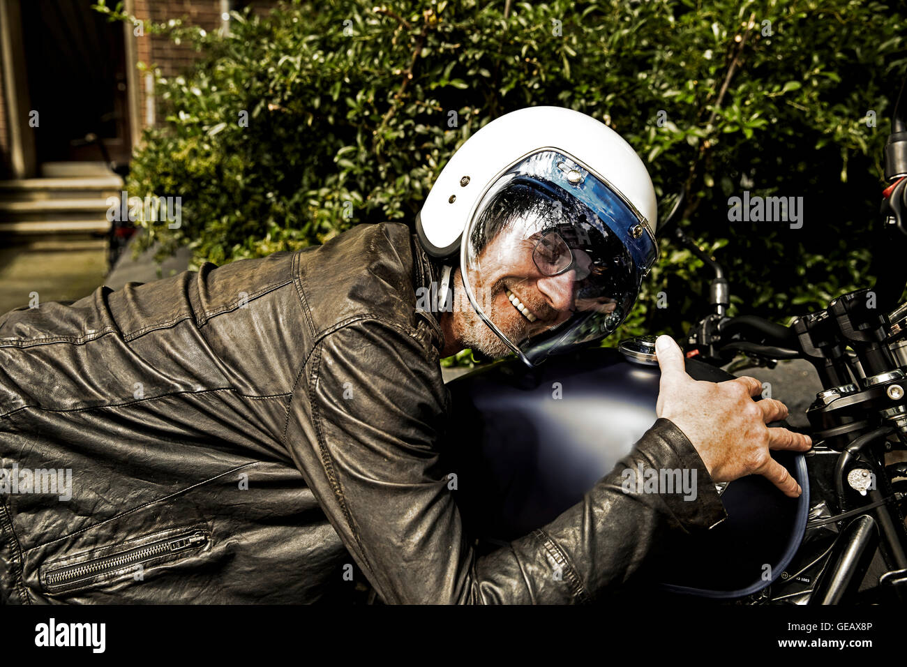 Smiling man wearing motorcycle helmet and leather jacket lying on his ...