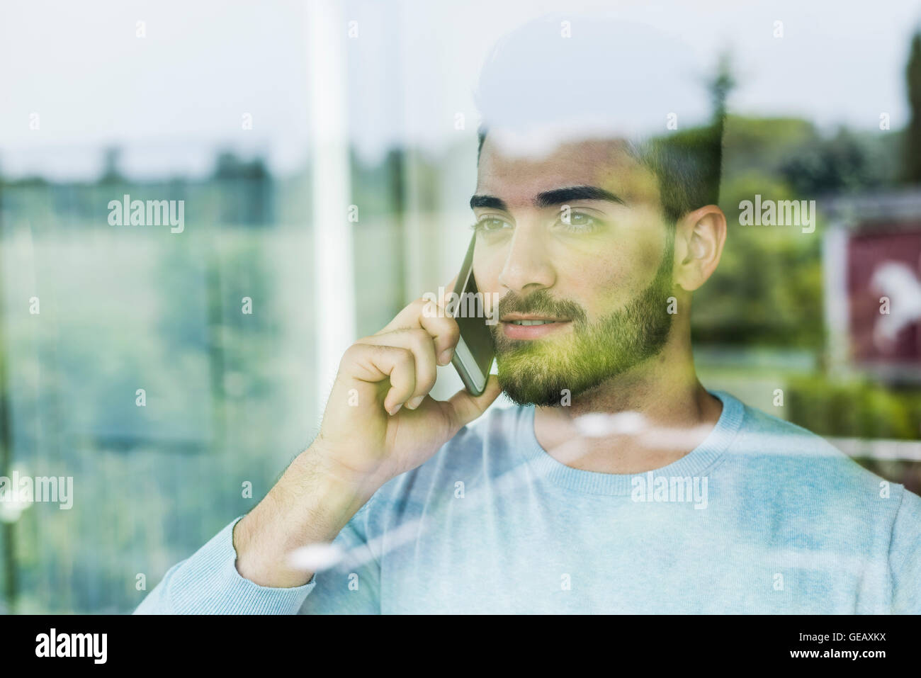 Young man with cell phone looking out of window Stock Photo - Alamy