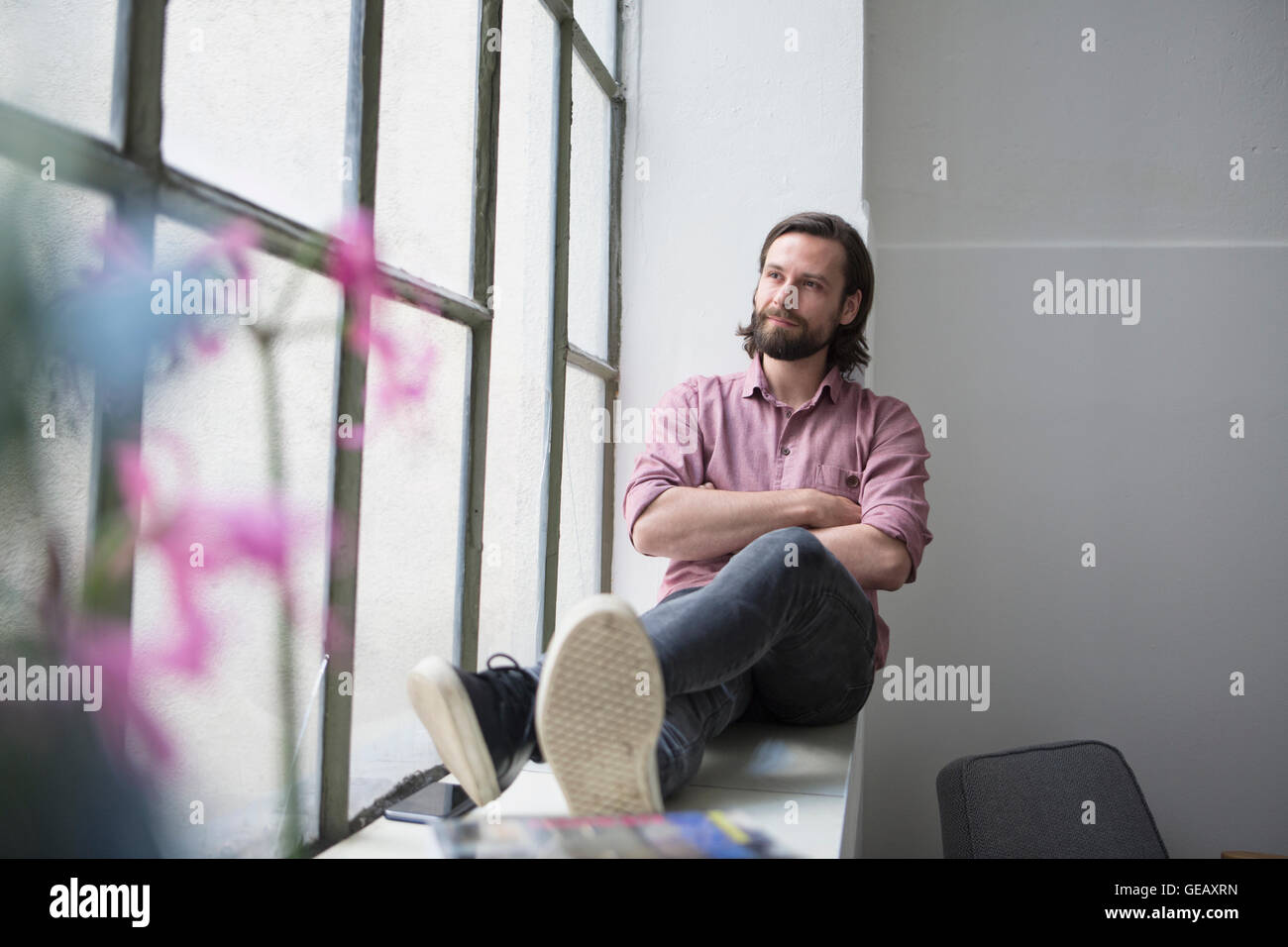 Man sitting on window sill looking out of window Stock Photo - Alamy