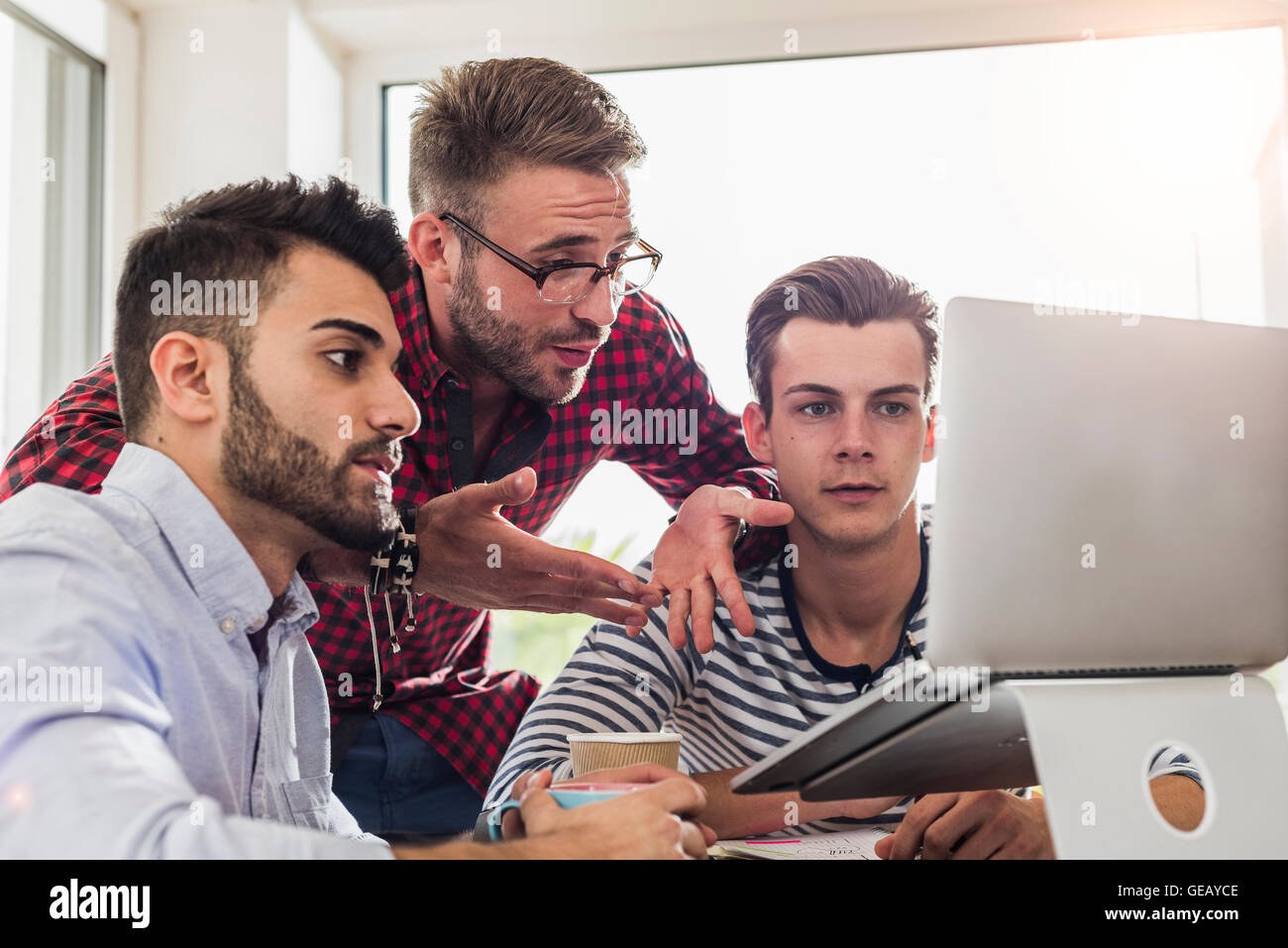 Three young professionals sharing laptop in office Stock Photo - Alamy