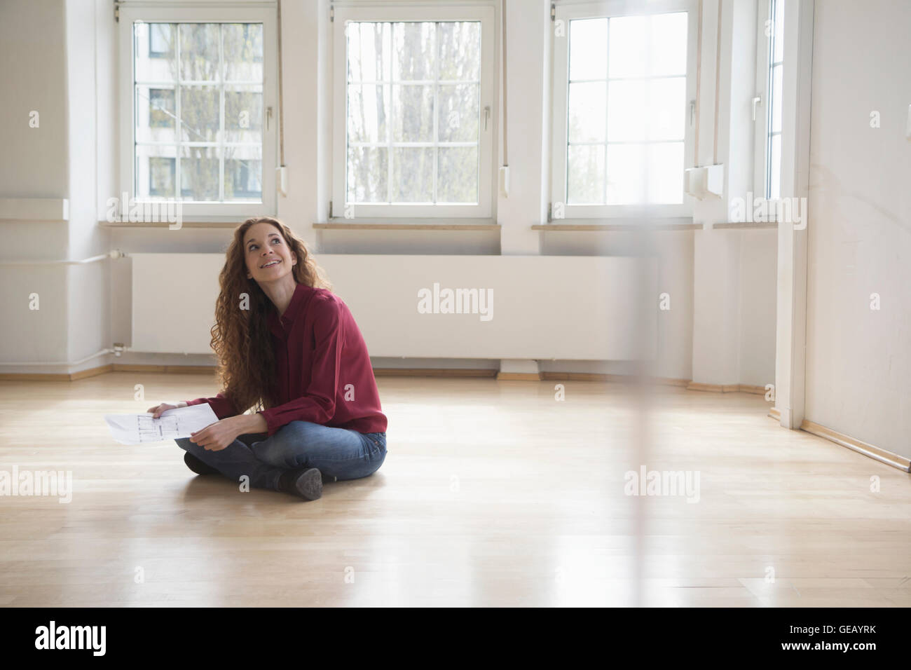 Woman sitting on floor in empty apartment looking around Stock Photo ...