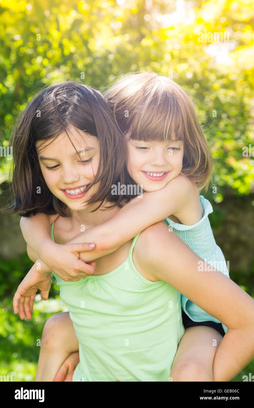 Girl giving her little sister a piggyback ride in the garden Stock ...