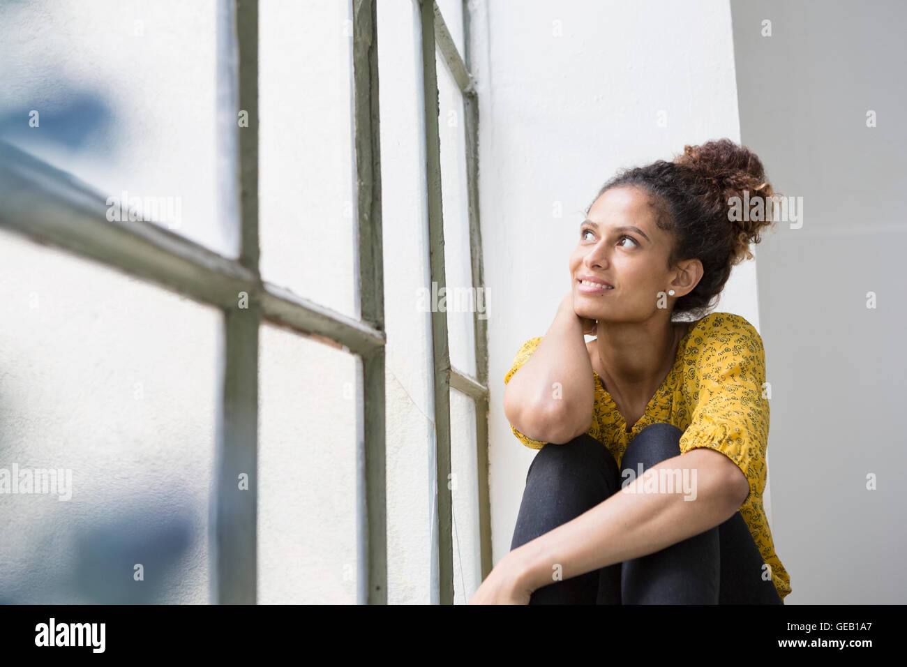 Young woman sitting on window sill, looking out of window Stock Photo ...