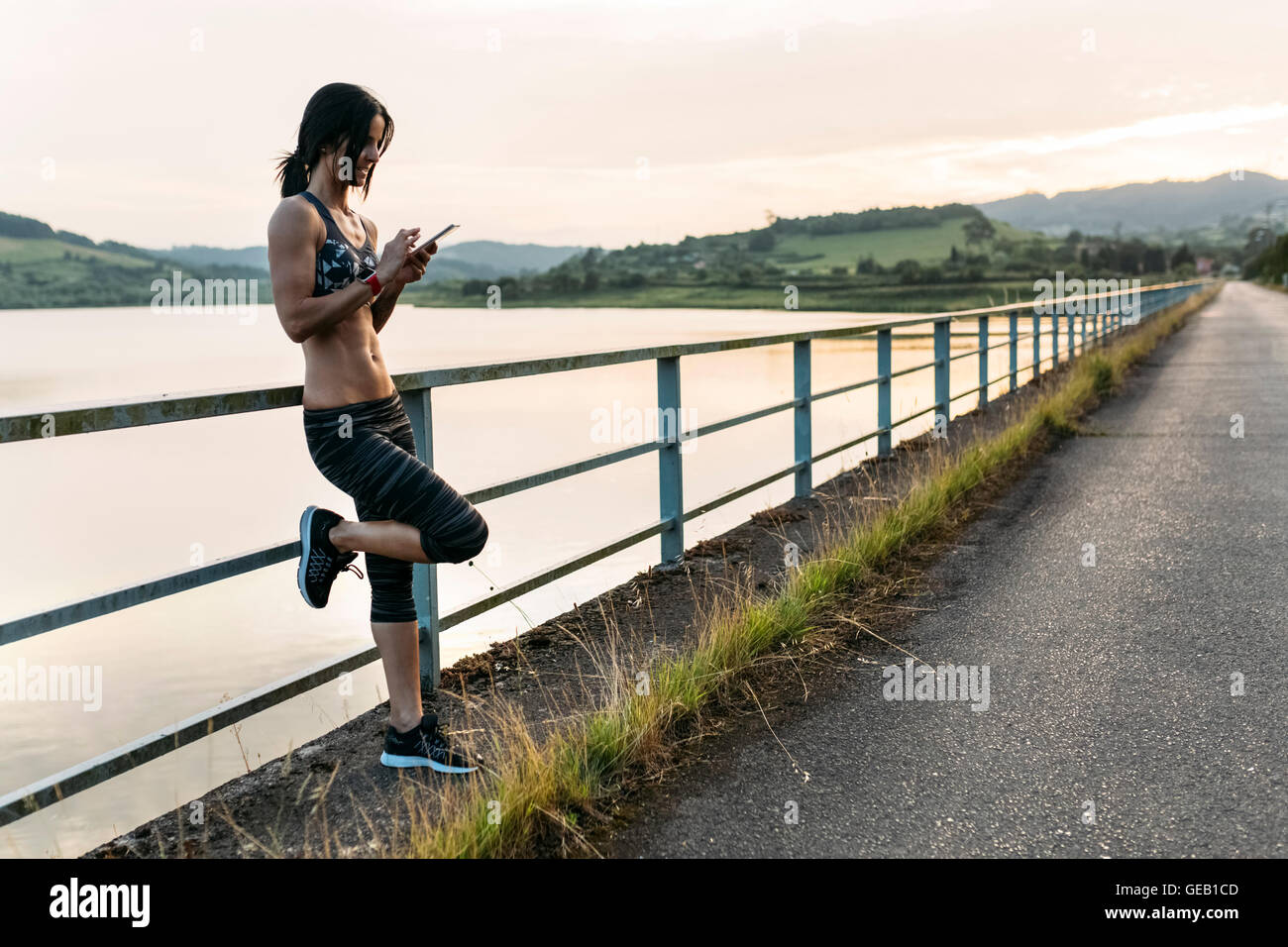 Female athlete checking smart phone leaning on railing Stock Photo - Alamy