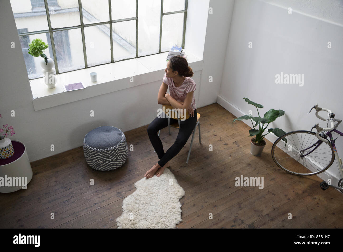 Young woman sitting on chair, looking out of window Stock Photo - Alamy