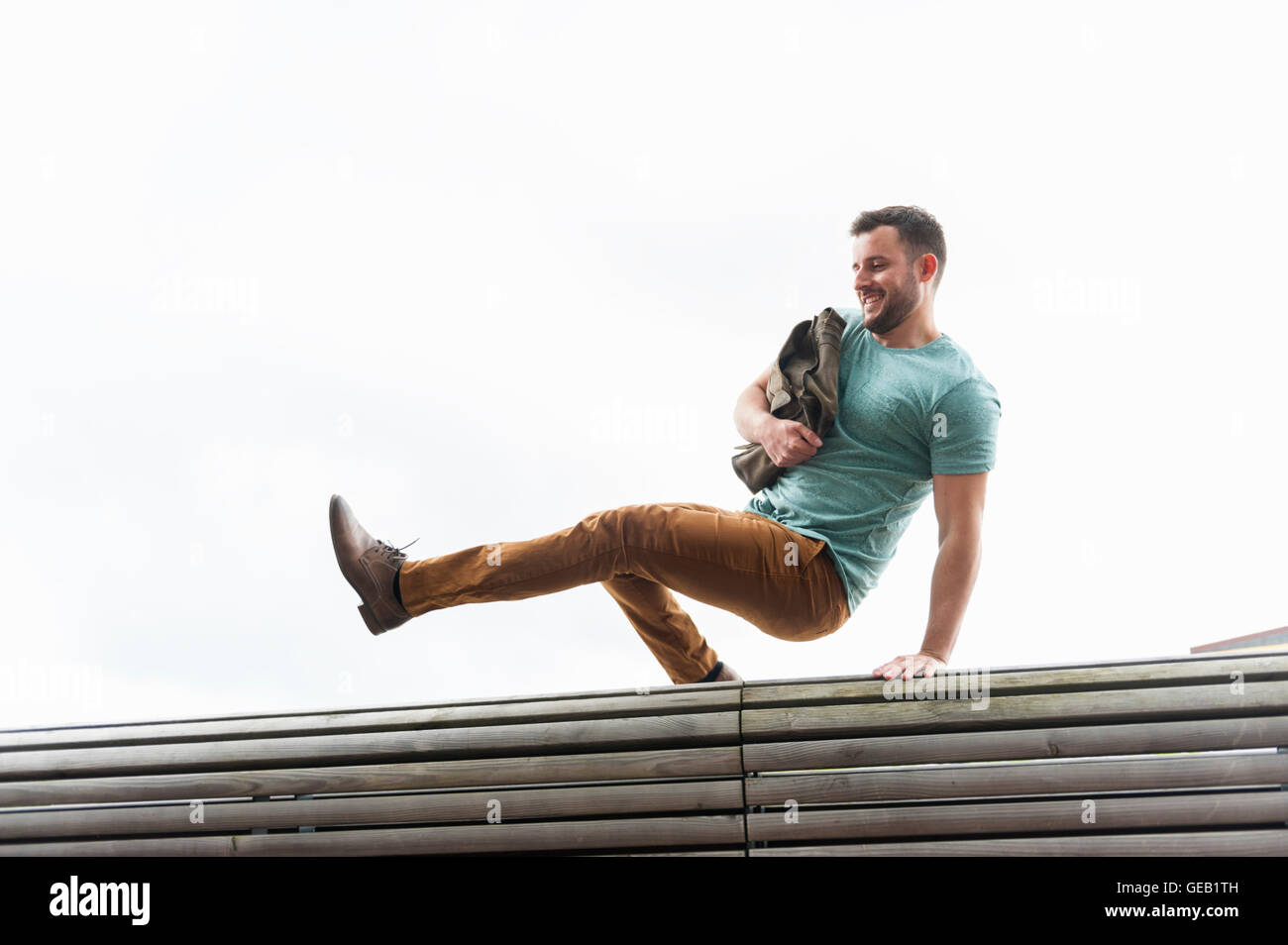 Young man with bag jumping over bench Stock Photo - Alamy