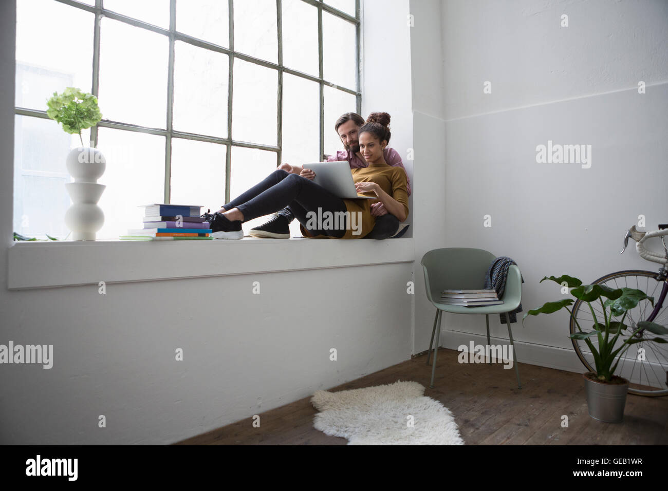 Young couple sitting on window sill using laptop Stock Photo - Alamy