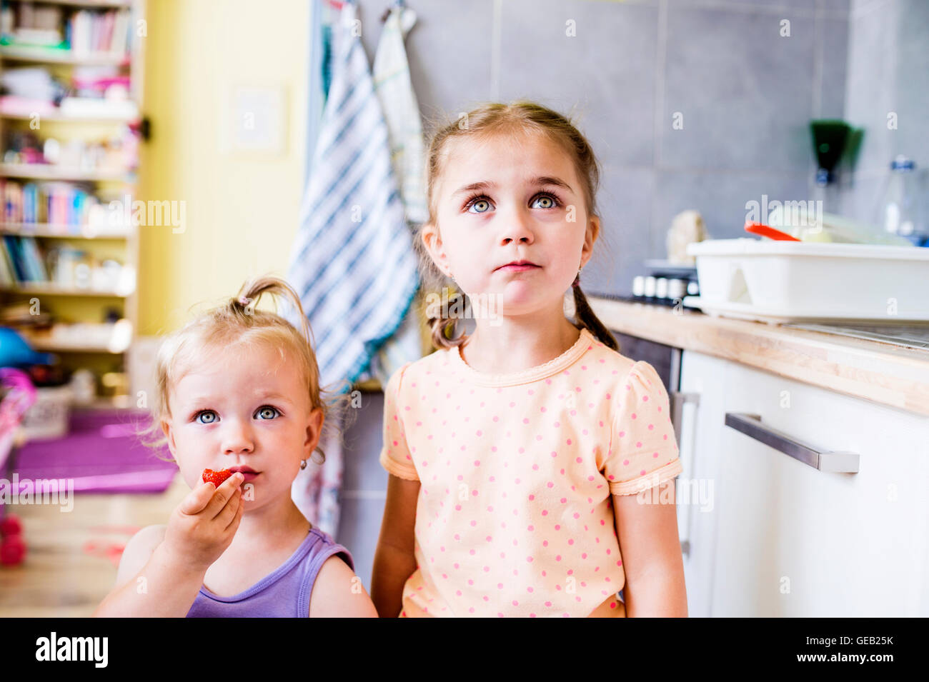 Two little sisters standing in kitchen, looking up Stock Photo - Alamy