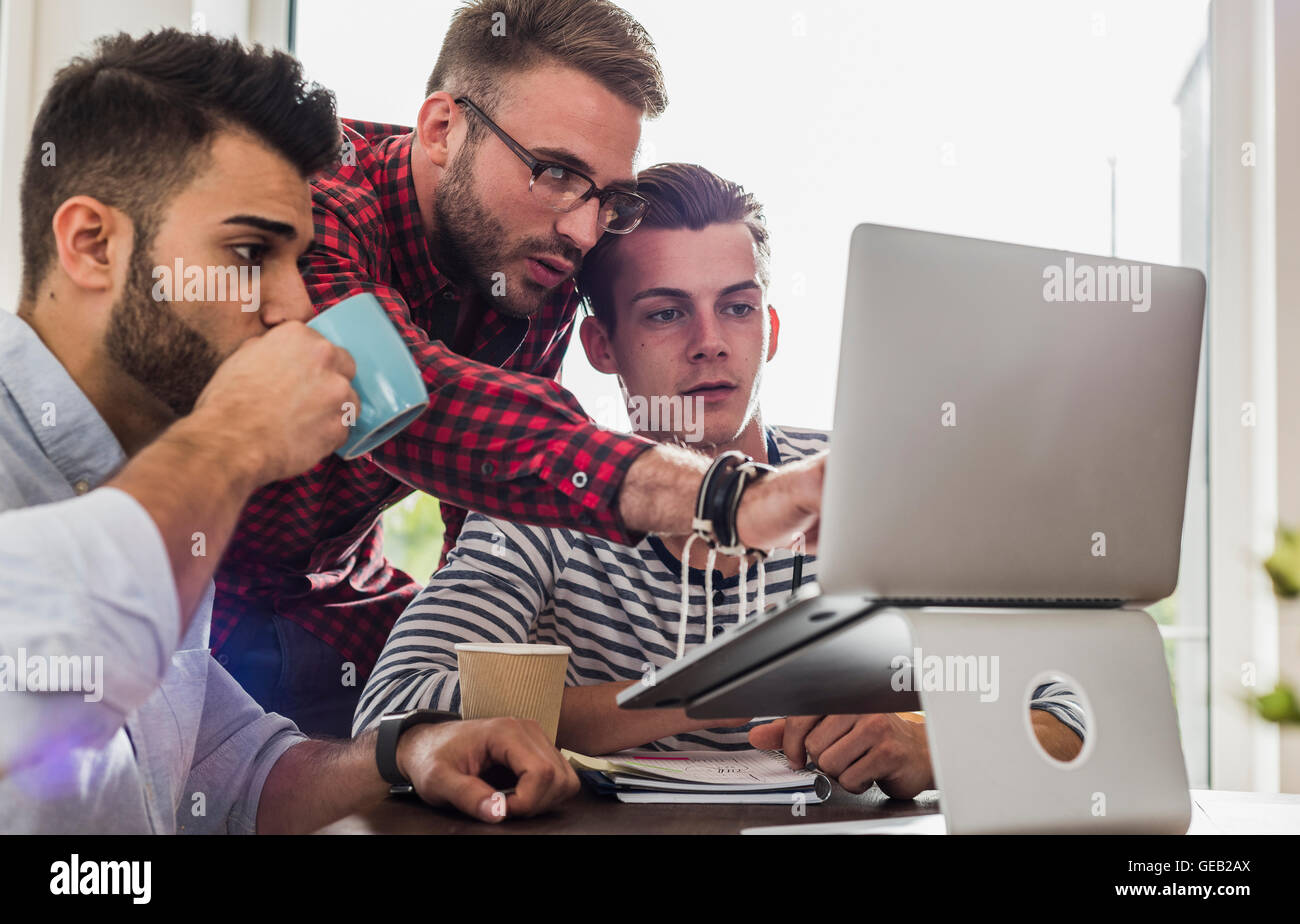 Three young professionals sharing laptop in office Stock Photo - Alamy