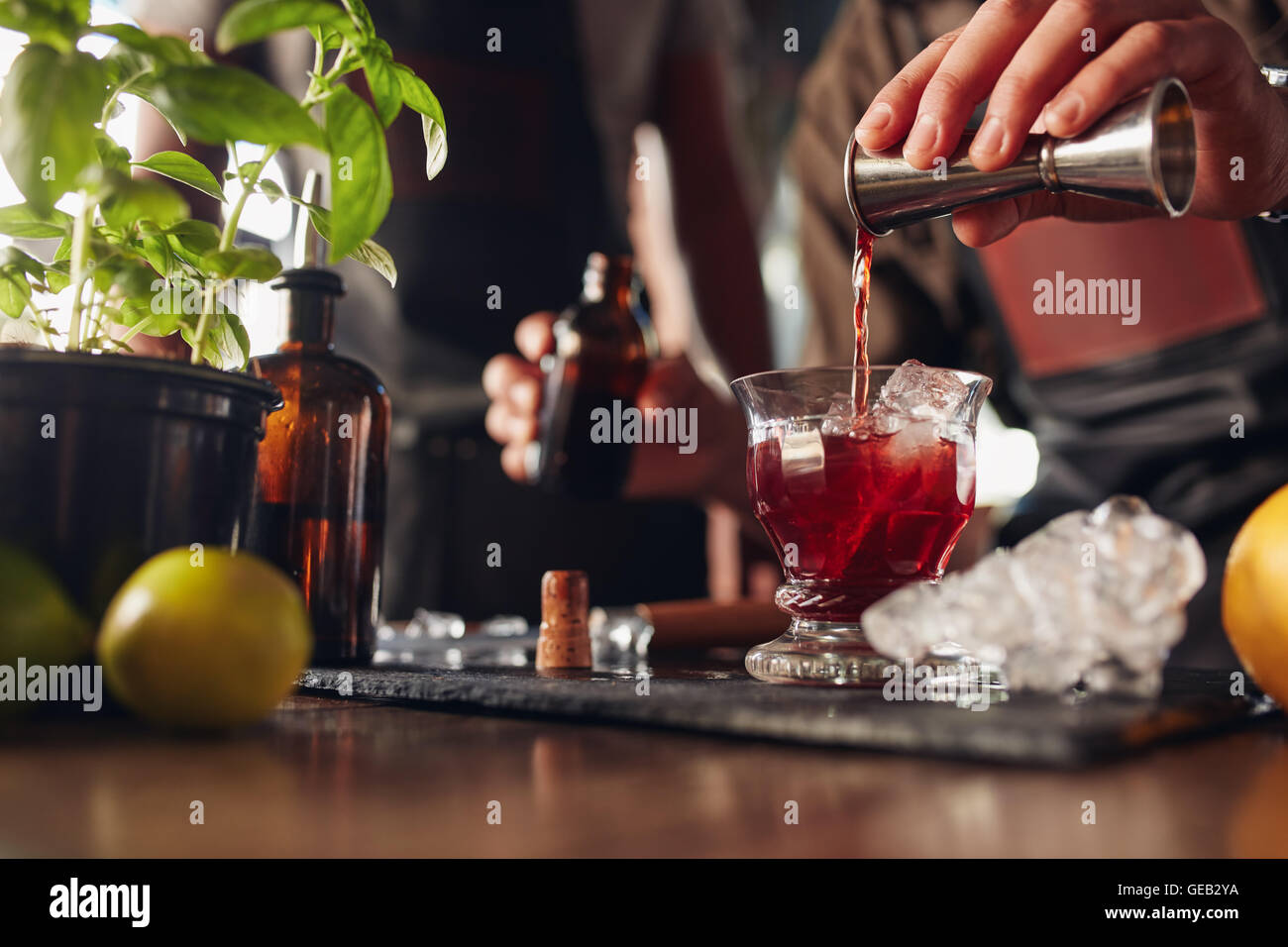 Close up shot of barman hand pouring drink from measuring cup into a cocktail glass filled with ...