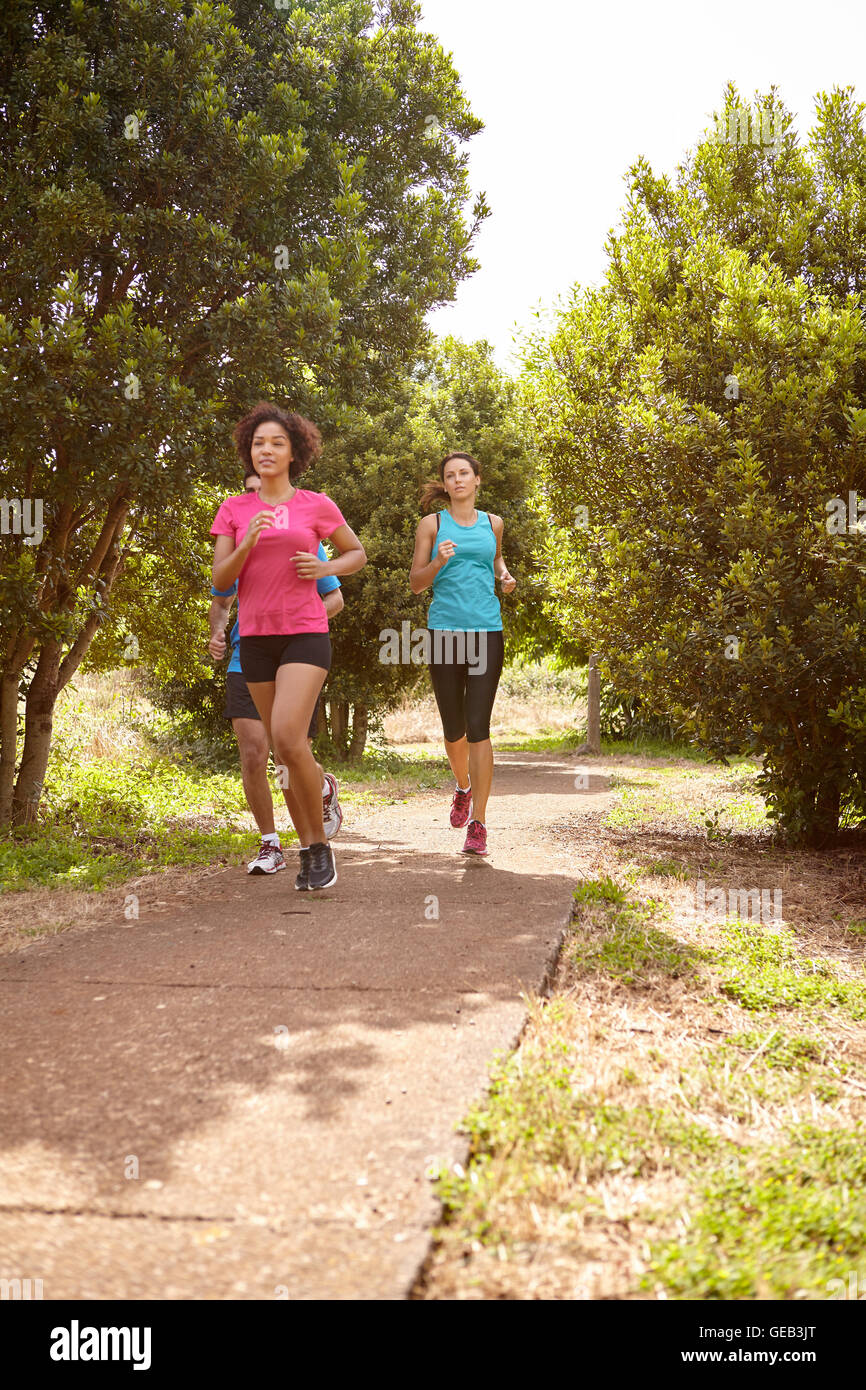 Three young runners on a paved jogging trail in daylight surrounded by ...