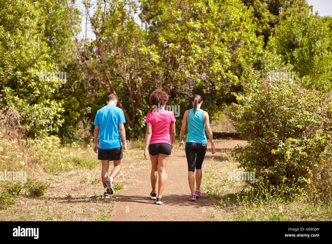 Three young runners walking on a paved jogging trail in daylight ...
