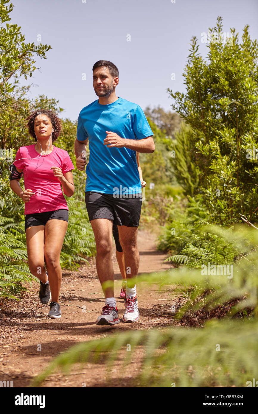 Three young joggers out for a run on a gravel path surrounded by bushes ...
