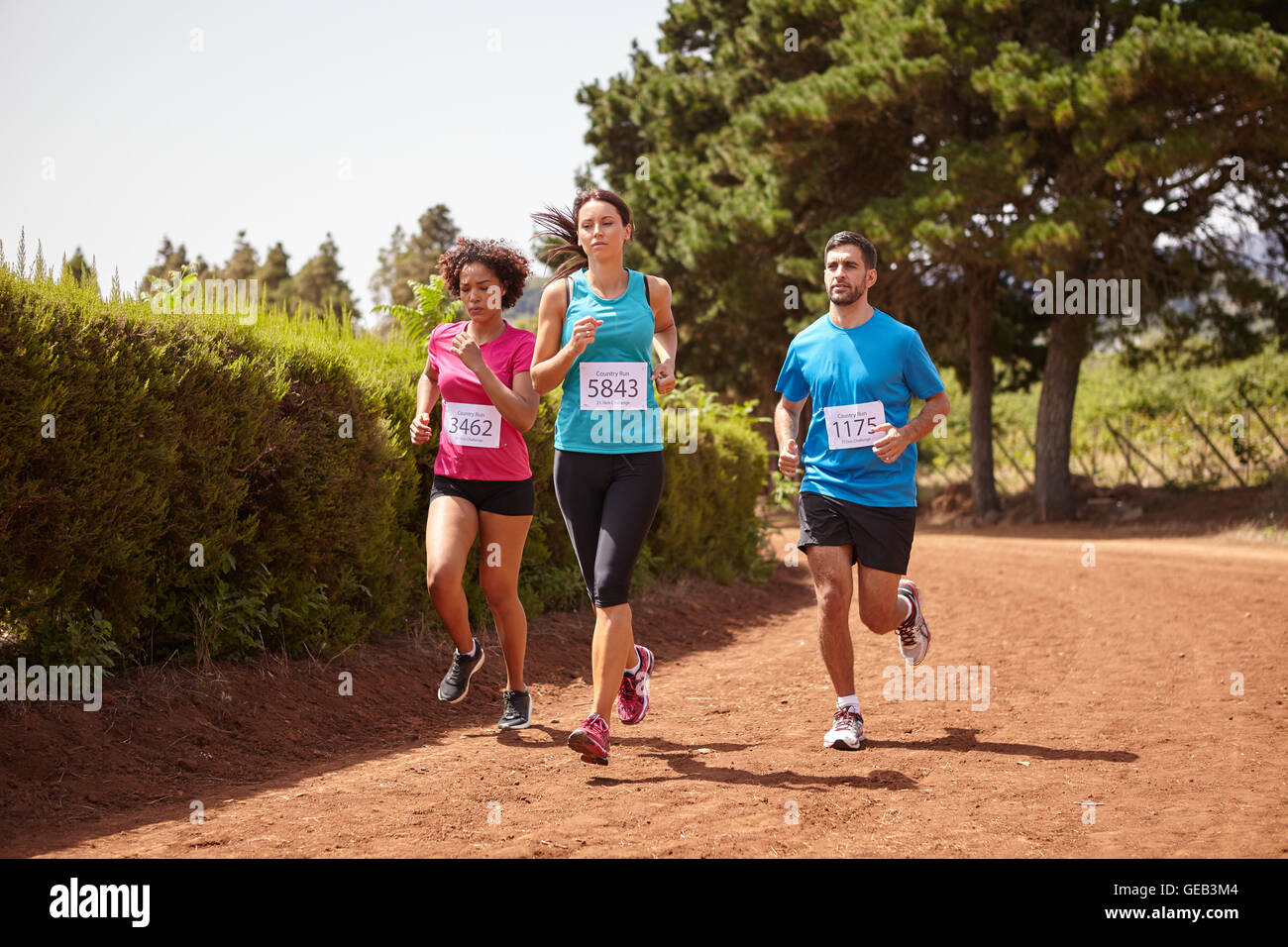 Three friends running in a race on a gravel path with trees behind them ...