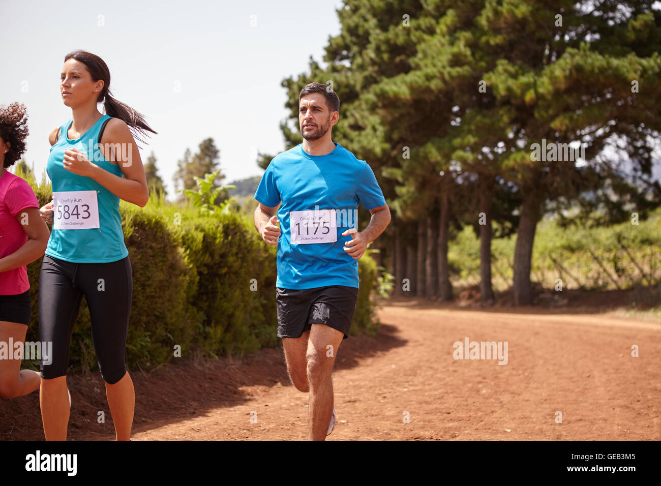 Three marathon runners in a race on a gravel path with trees behind ...