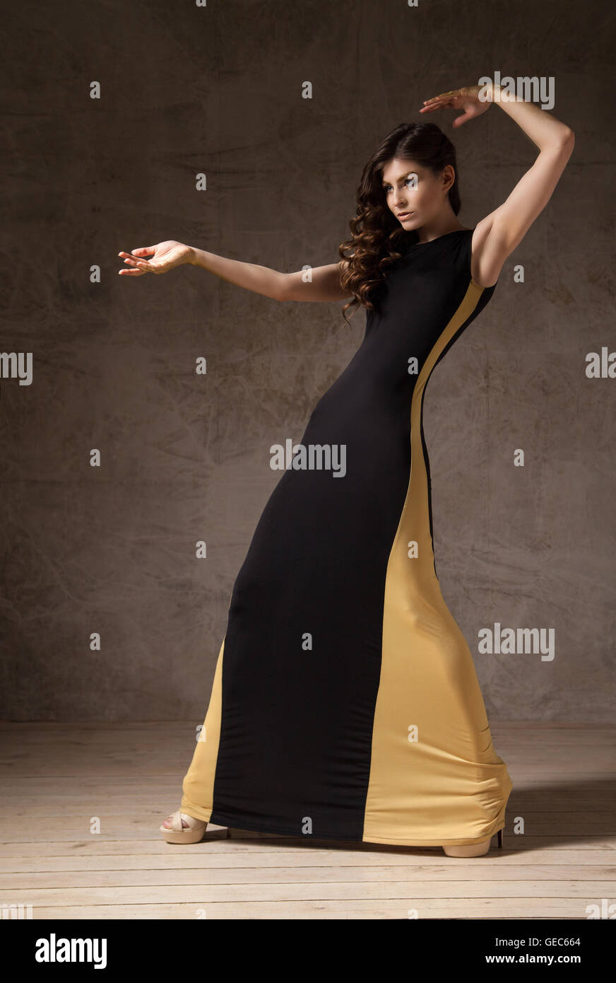 fashion model with wavy hair wearing long dress and gesturing by arms ...