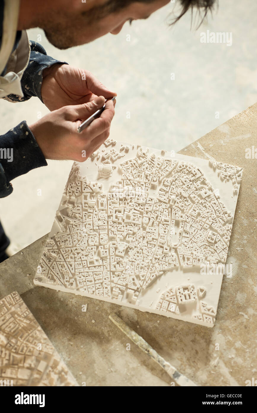 Man working on a fine component of a 3D city map model made of plaster ...
