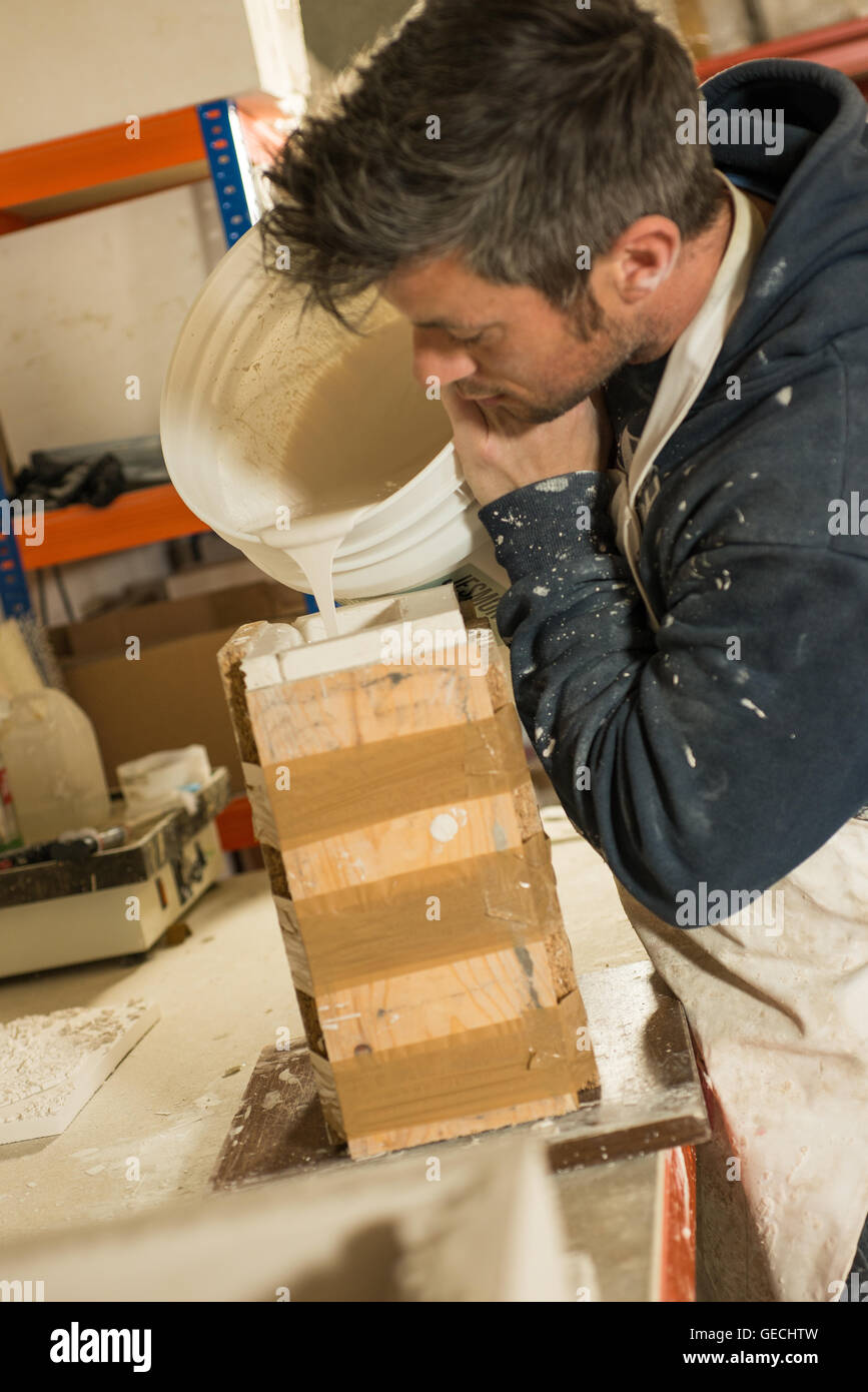 A man in plaster-splattered clothing pouring liquid plaster mixture ...