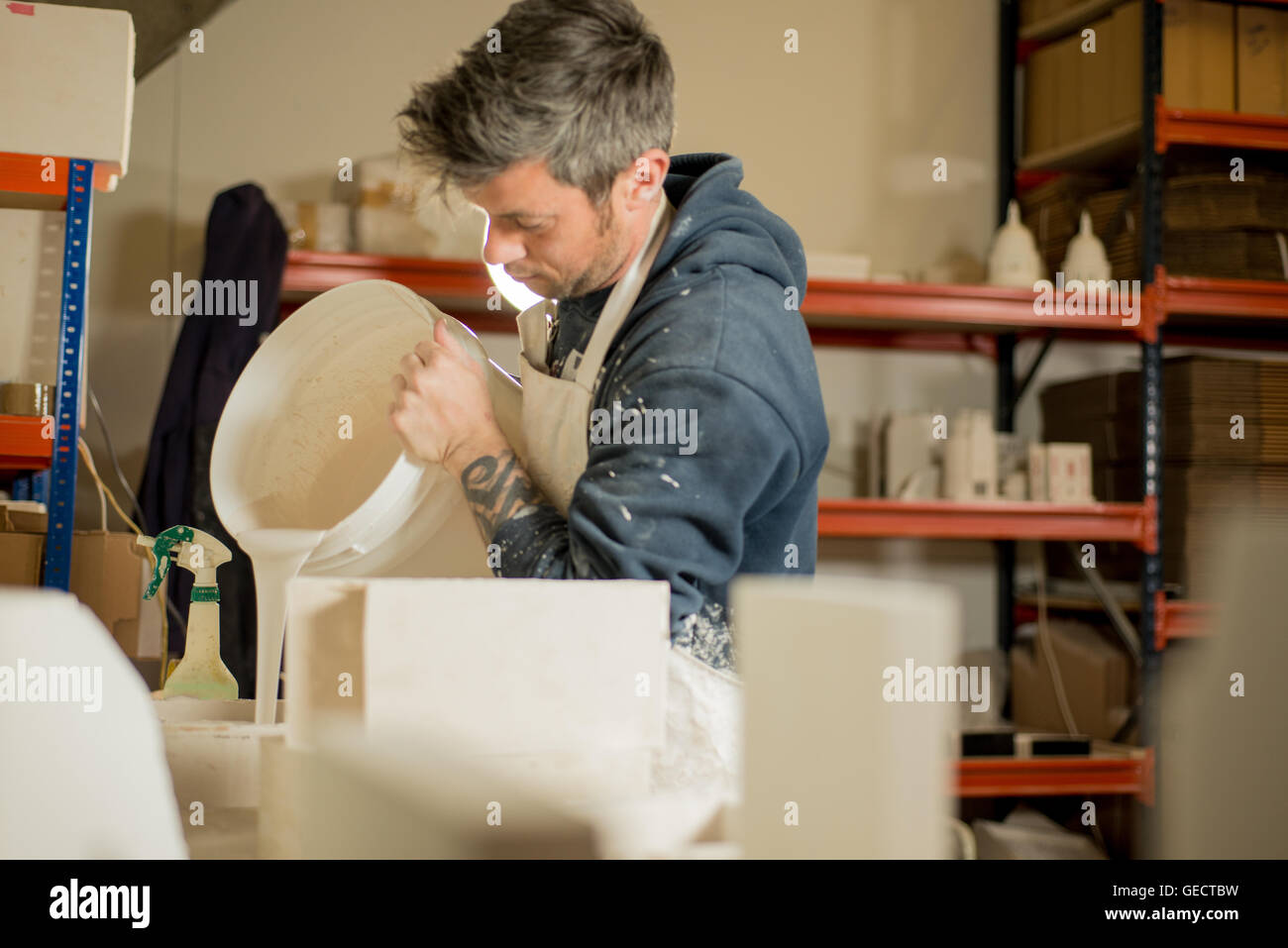 A man in plaster-splattered clothing pouring plaster mixture into a ...