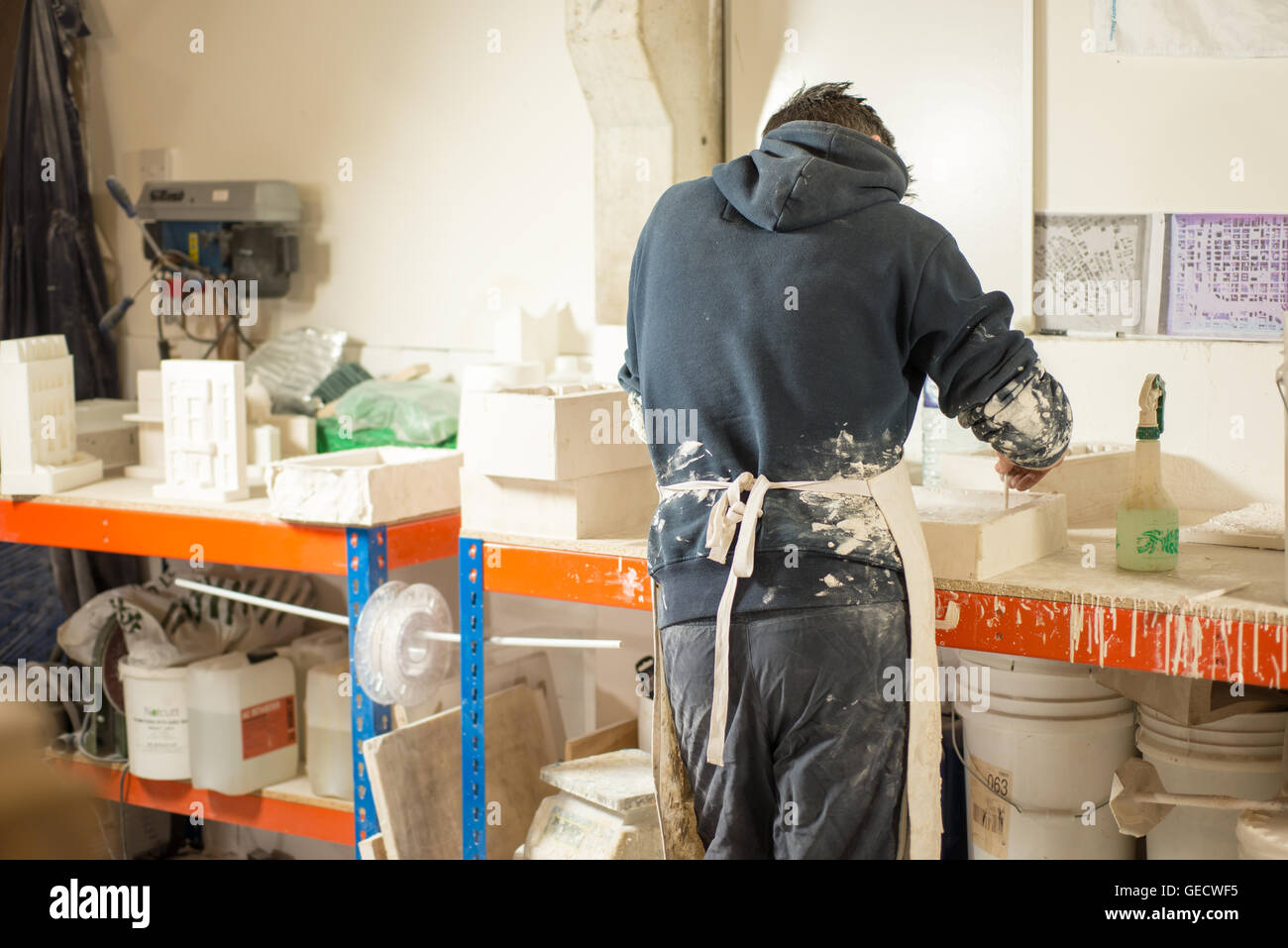 A man in plaster-splattered clothing and apron with back turned levels ...