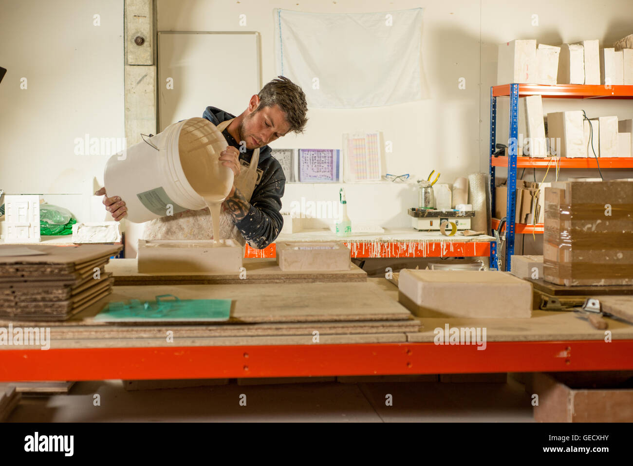 A man in plaster-splattered clothing and apron pours gypsum plaster ...