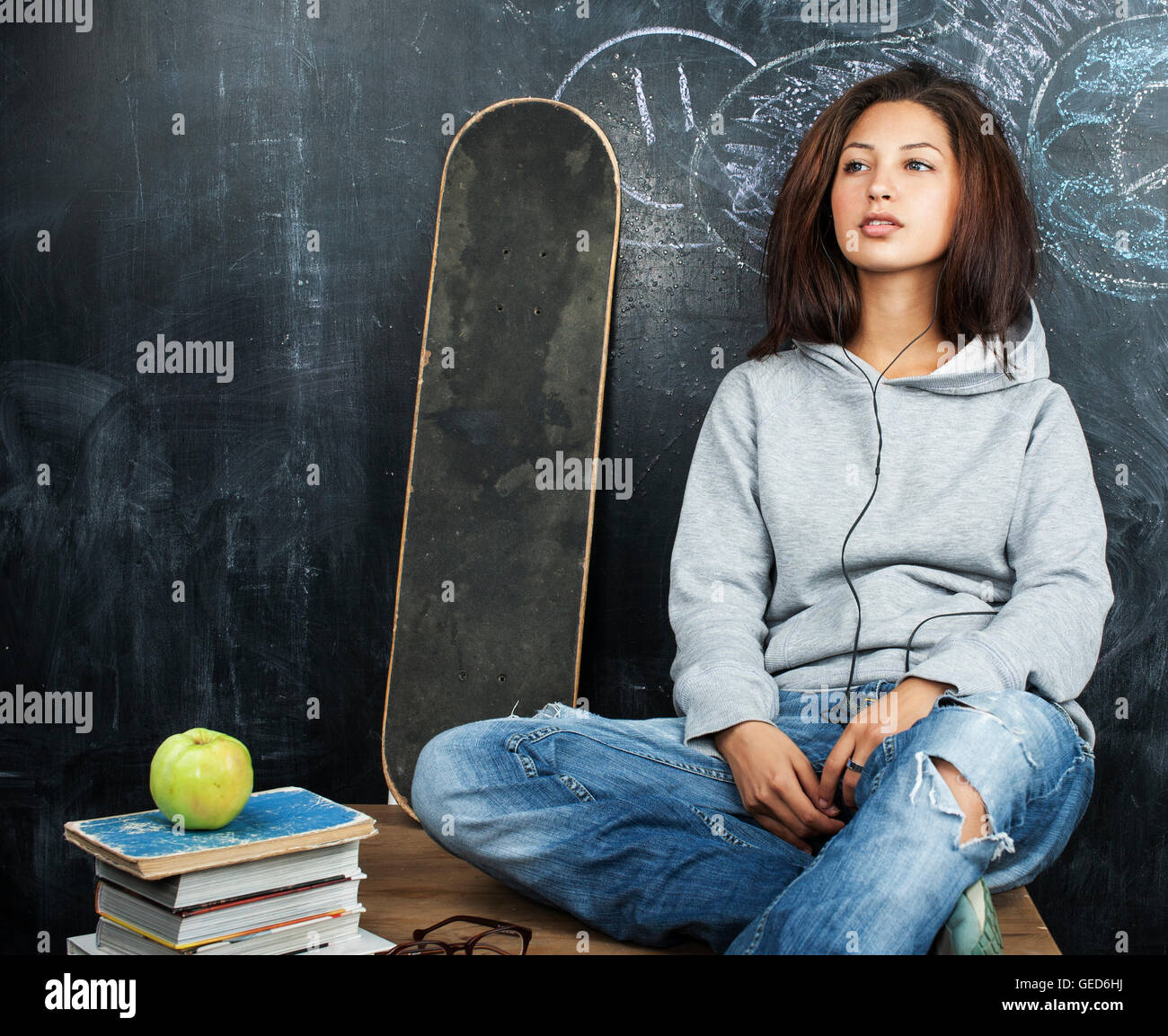 young cute teenage girl in classroom at blackboard seating on table ...