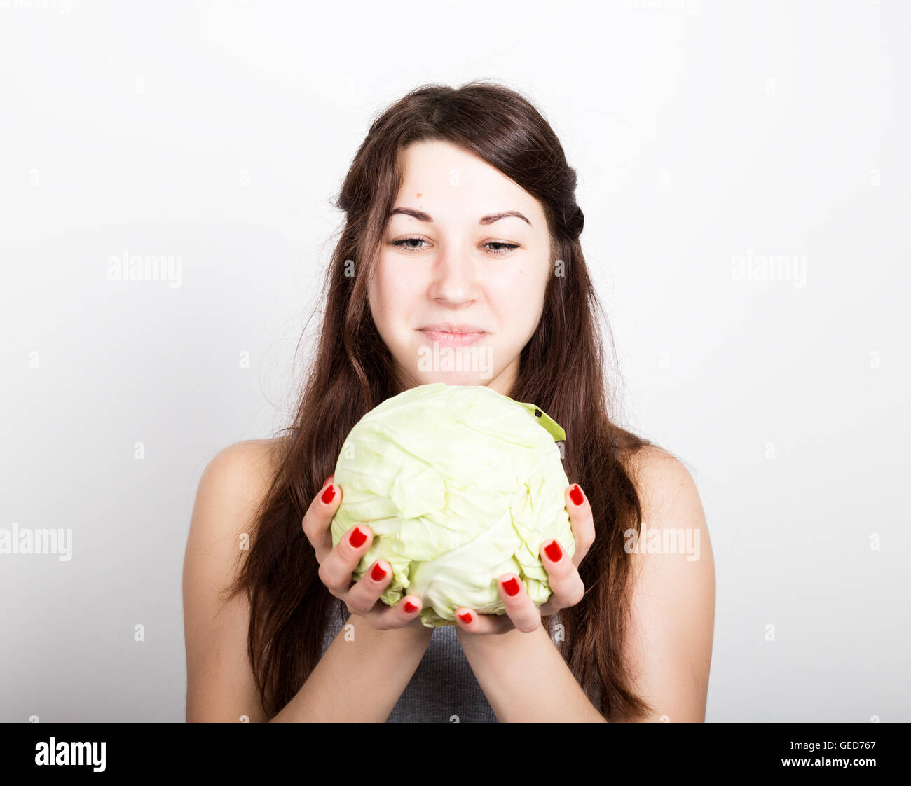 beautiful young woman eating an vegetables. holding cabbage, she stares ...
