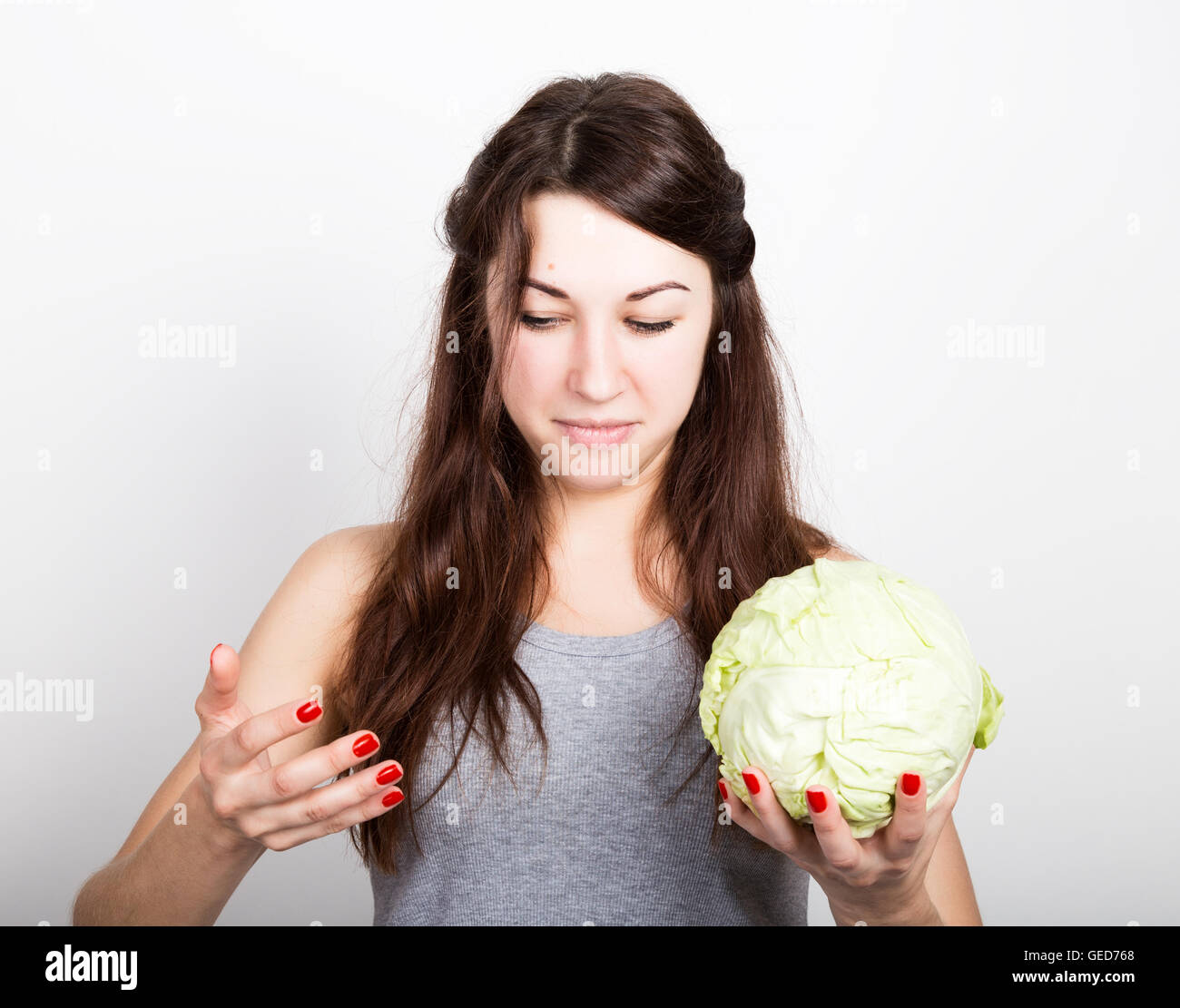 beautiful young woman eating an vegetables. holding cabbage, she stares ...
