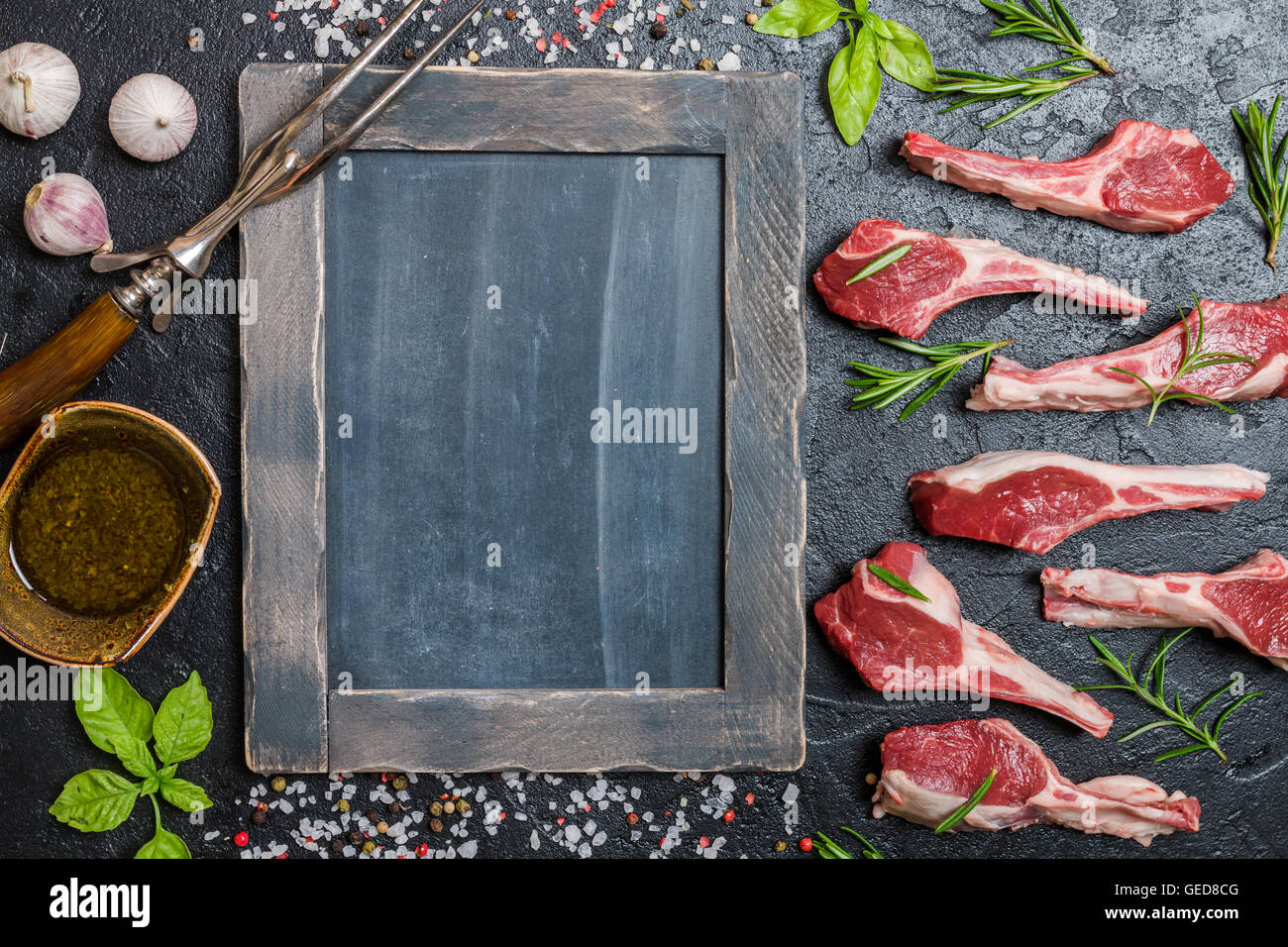 Raw lamb chops with salt, pepper and rosemary over black background ...
