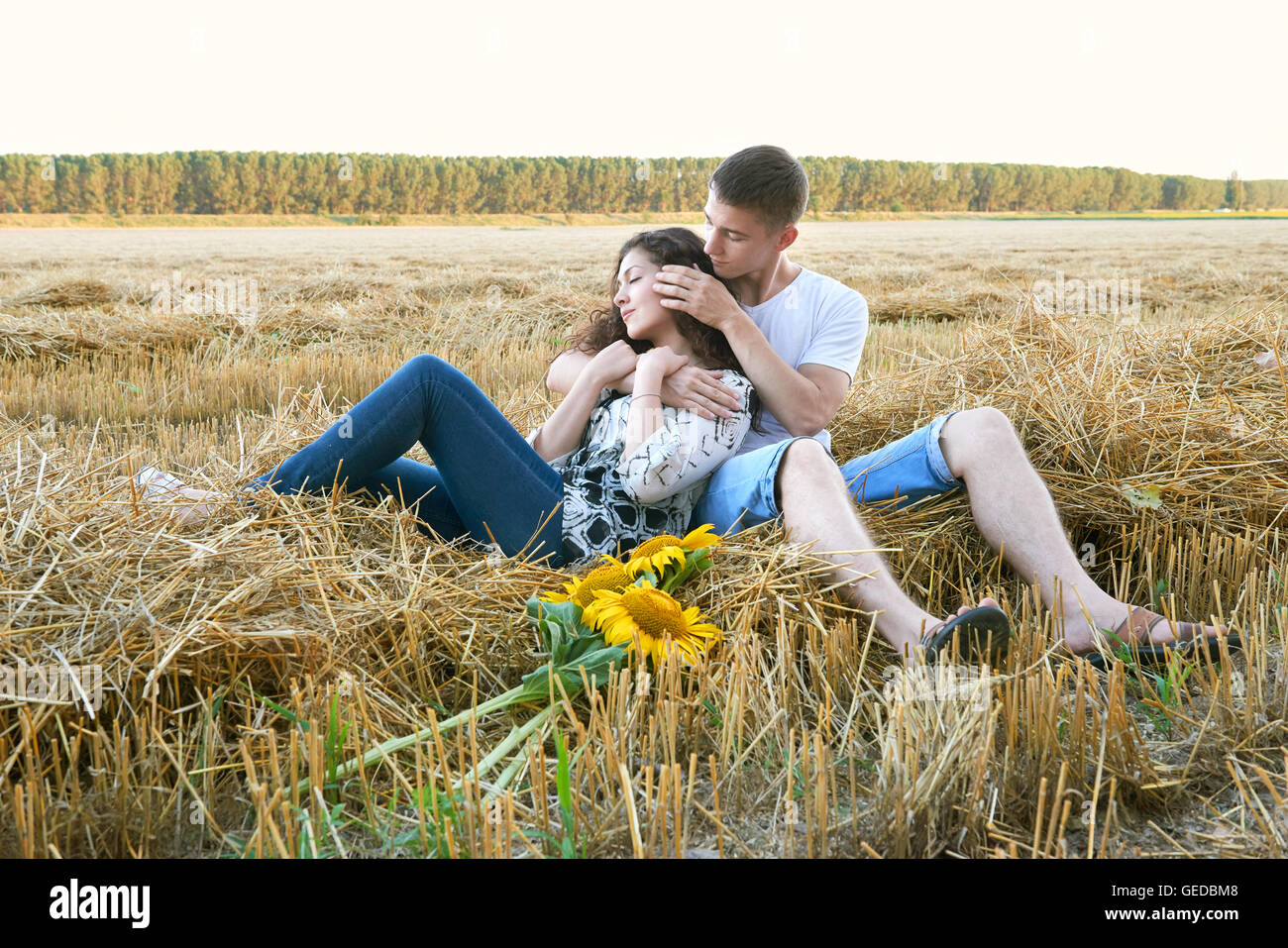 happy young couple sit in wheaten field at evening, romantic people ...