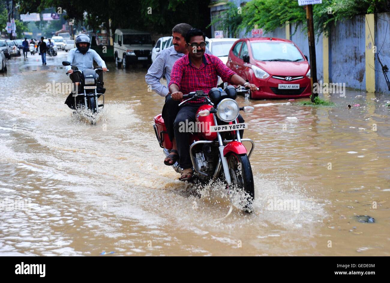 Allahabad, India. 25th July, 2016. People ride bike trough waterlogged ...