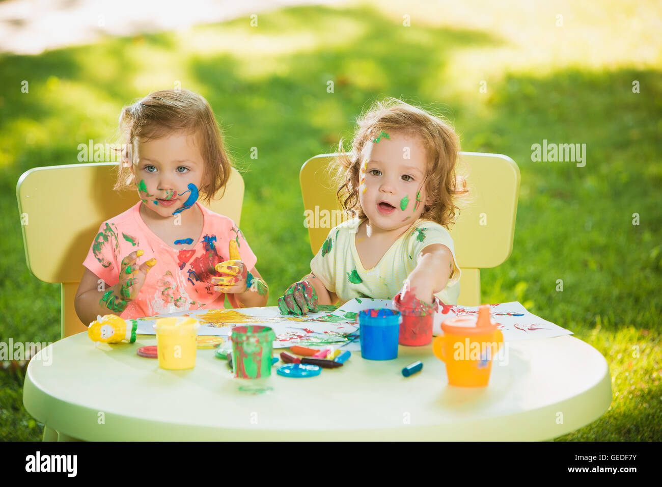Two-year old girls painting with poster paintings together against ...