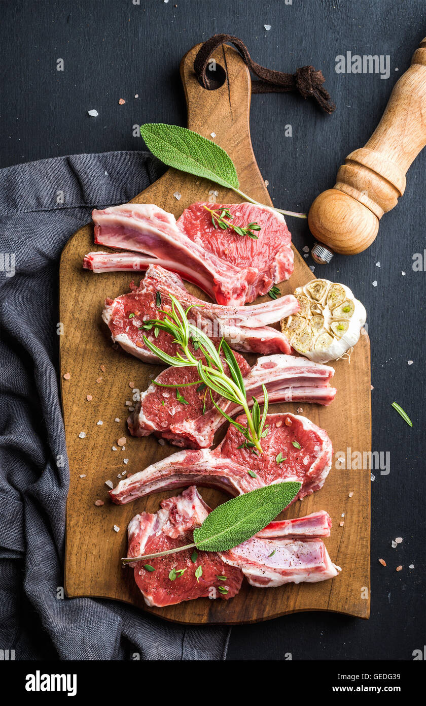 Raw uncooked lamb chops with herbs and spices on rustic wooden board ...