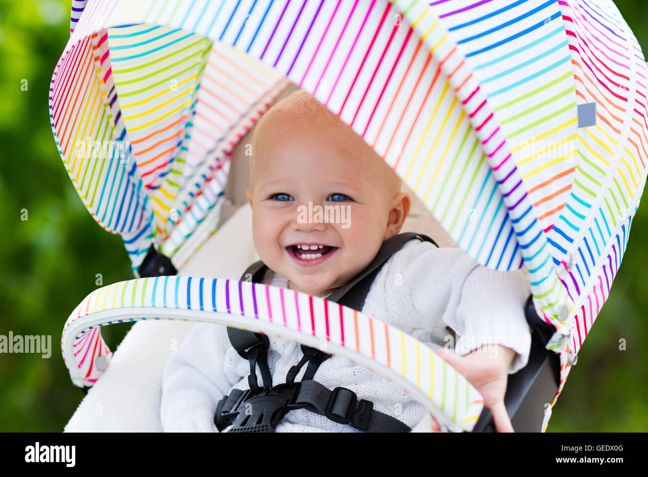 Baby boy in white sweater sitting in white stroller on a walk in park ...