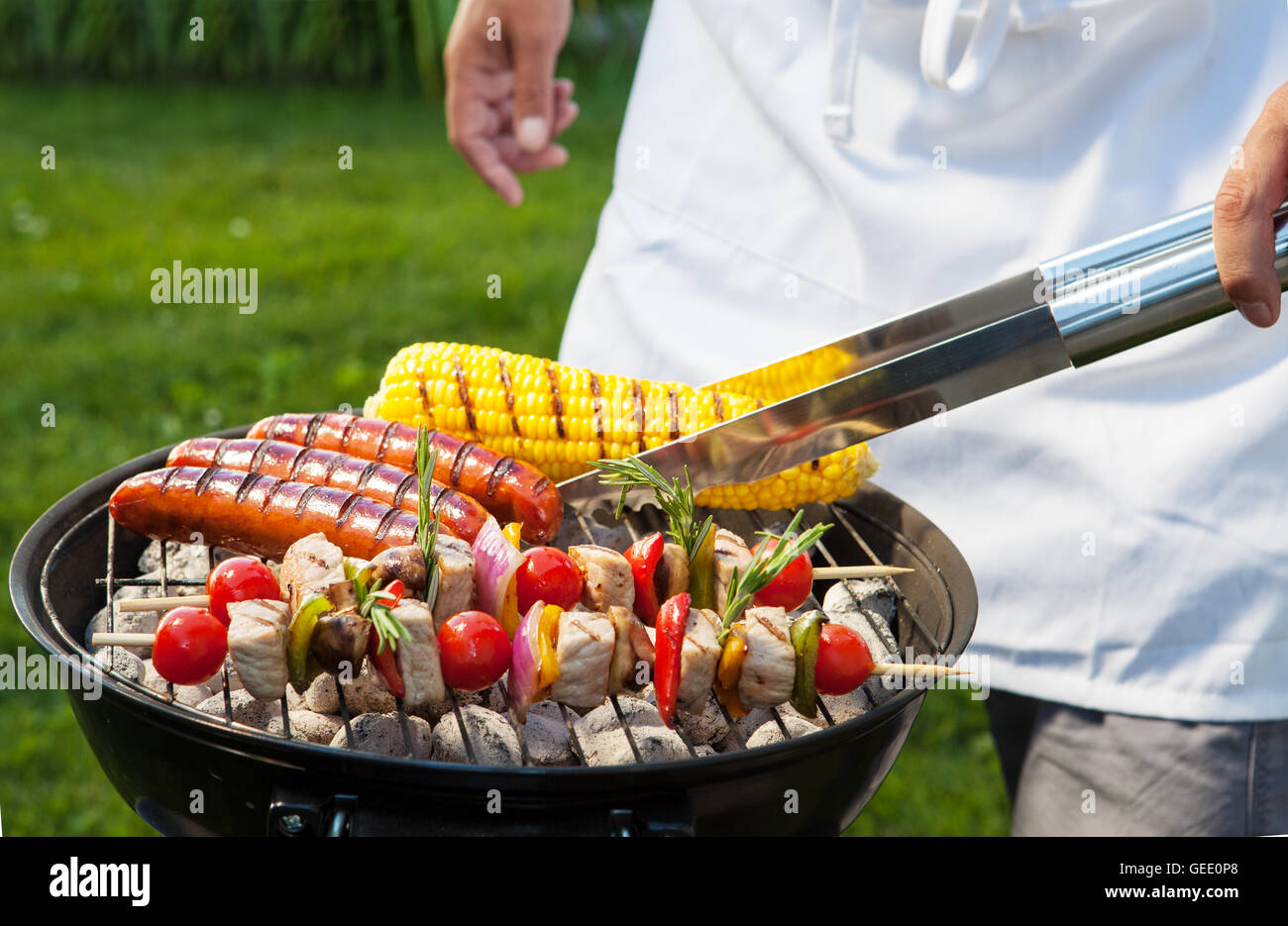 Man with tongs cooking on a back yard barbecue Stock Photo - Alamy