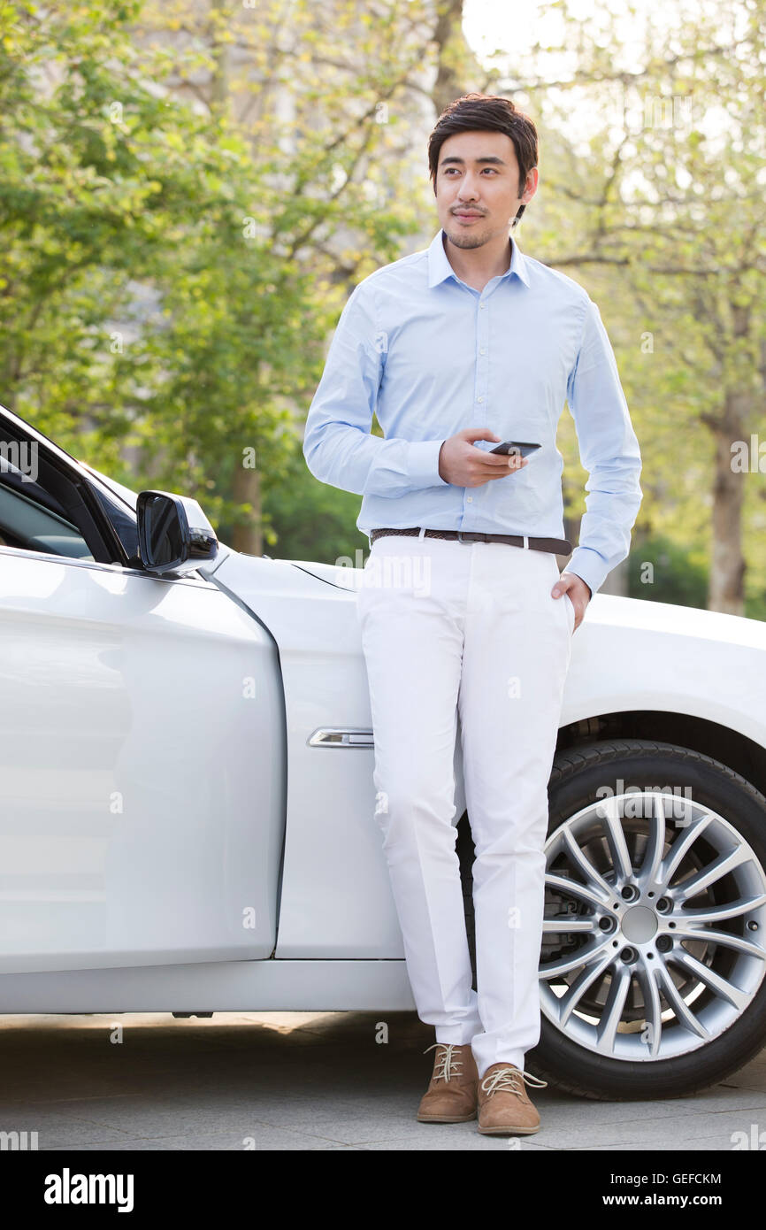Young Chinese man leaning on car with smart phone Stock Photo - Alamy