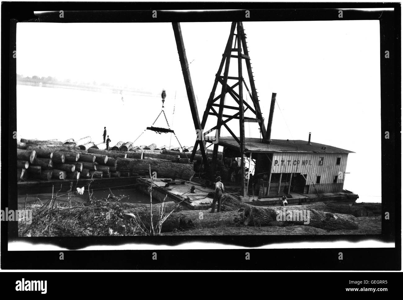 A derrick boat is used to load logs onto a boat, showcasing the early ...