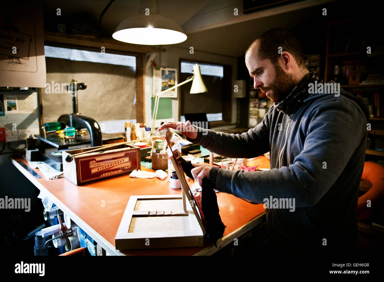 A sign writer at a workshop bench holding a sign Stock Photo - Alamy