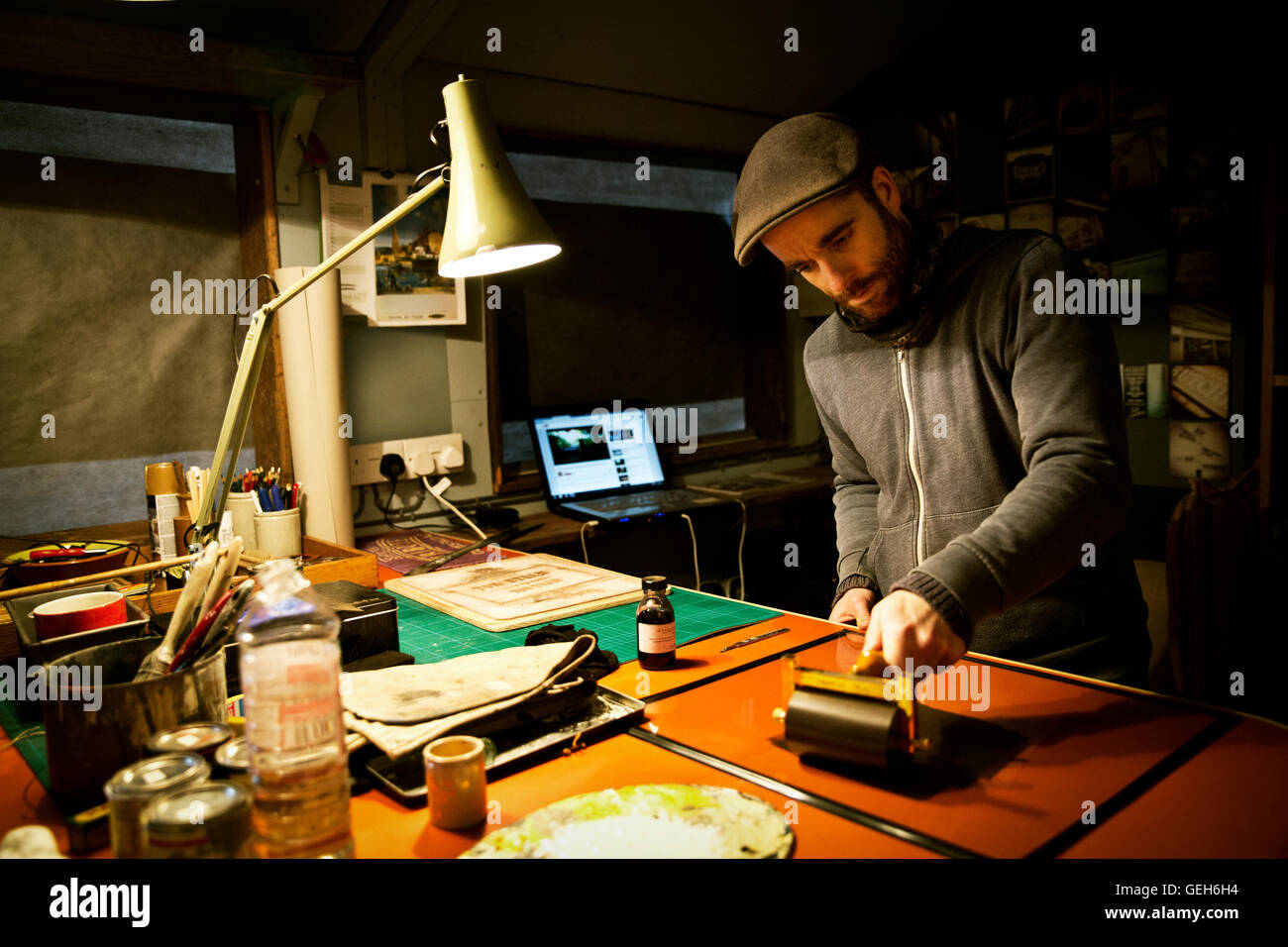 A sign maker rolling ink across the cut raised surface of linoleum ...