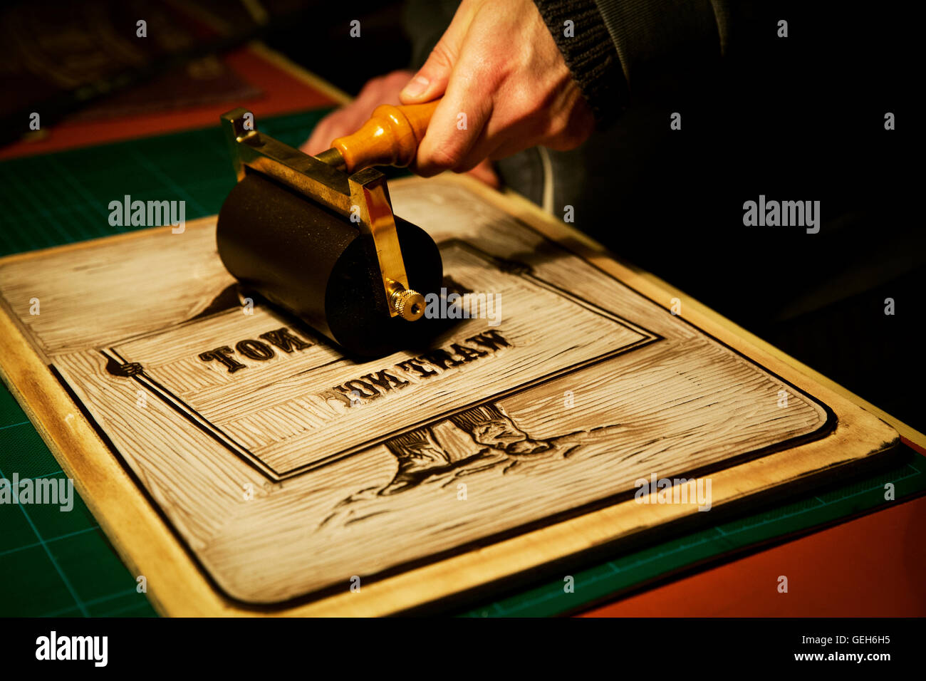 A sign maker rolling ink across the cut raised surface of linoleum ...
