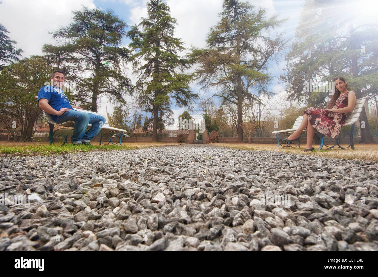 Low perspective view of a couple sitting apart on park benches with ...