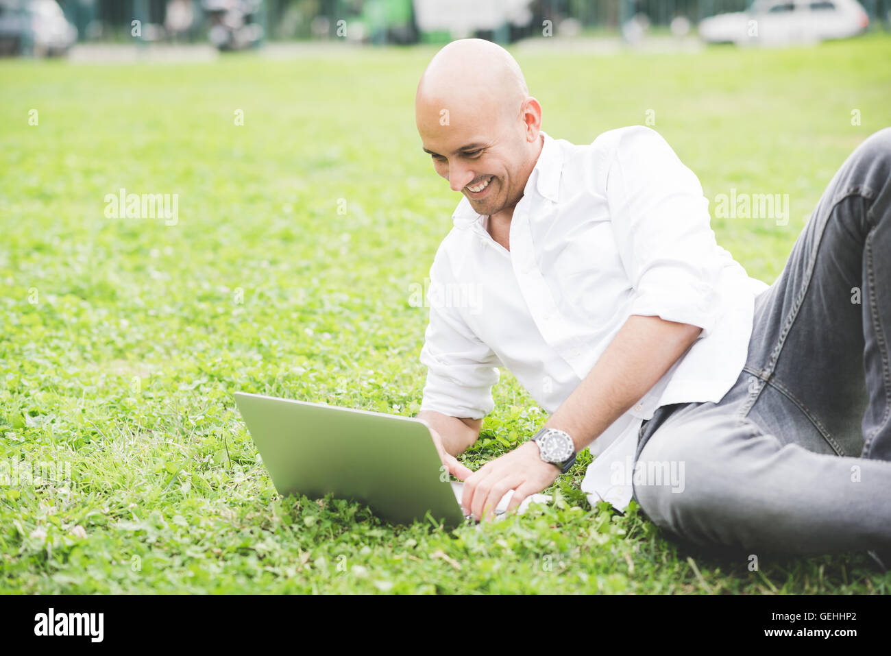 Young handsome caucasian bald business man sitting in a city park using ...